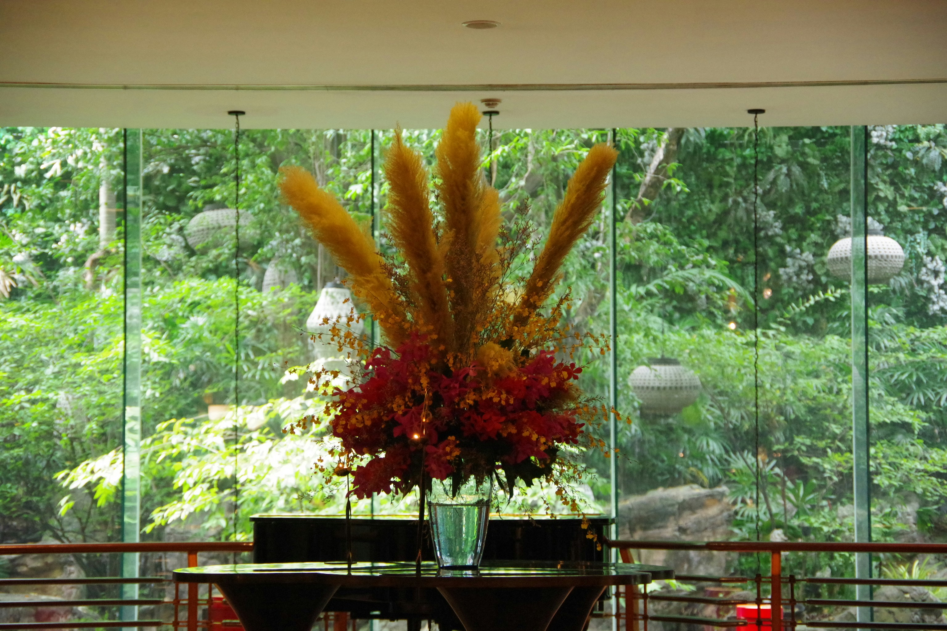 Vibrant floral arrangement featuring pampas grass and colorful blooms, set against a backdrop of lush greenery and glass walls.