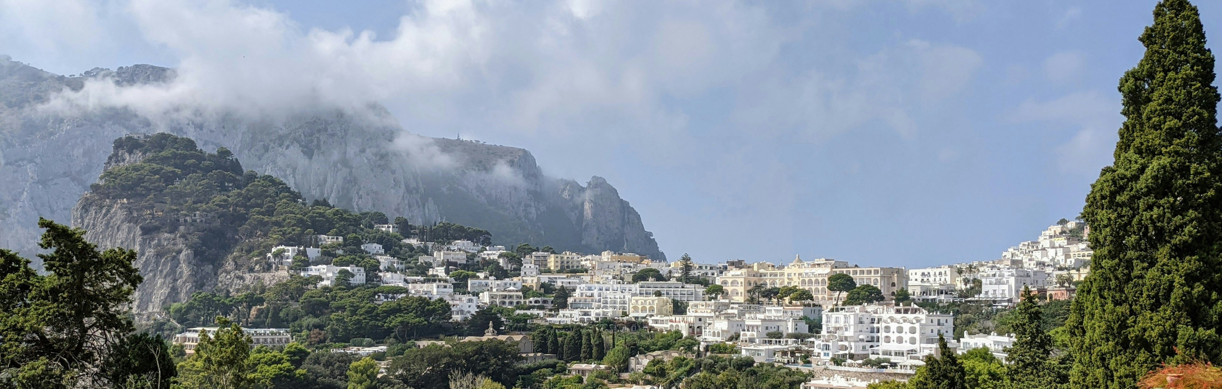Hillside town with white buildings nestled against a misty mountain backdrop under a clear blue sky.