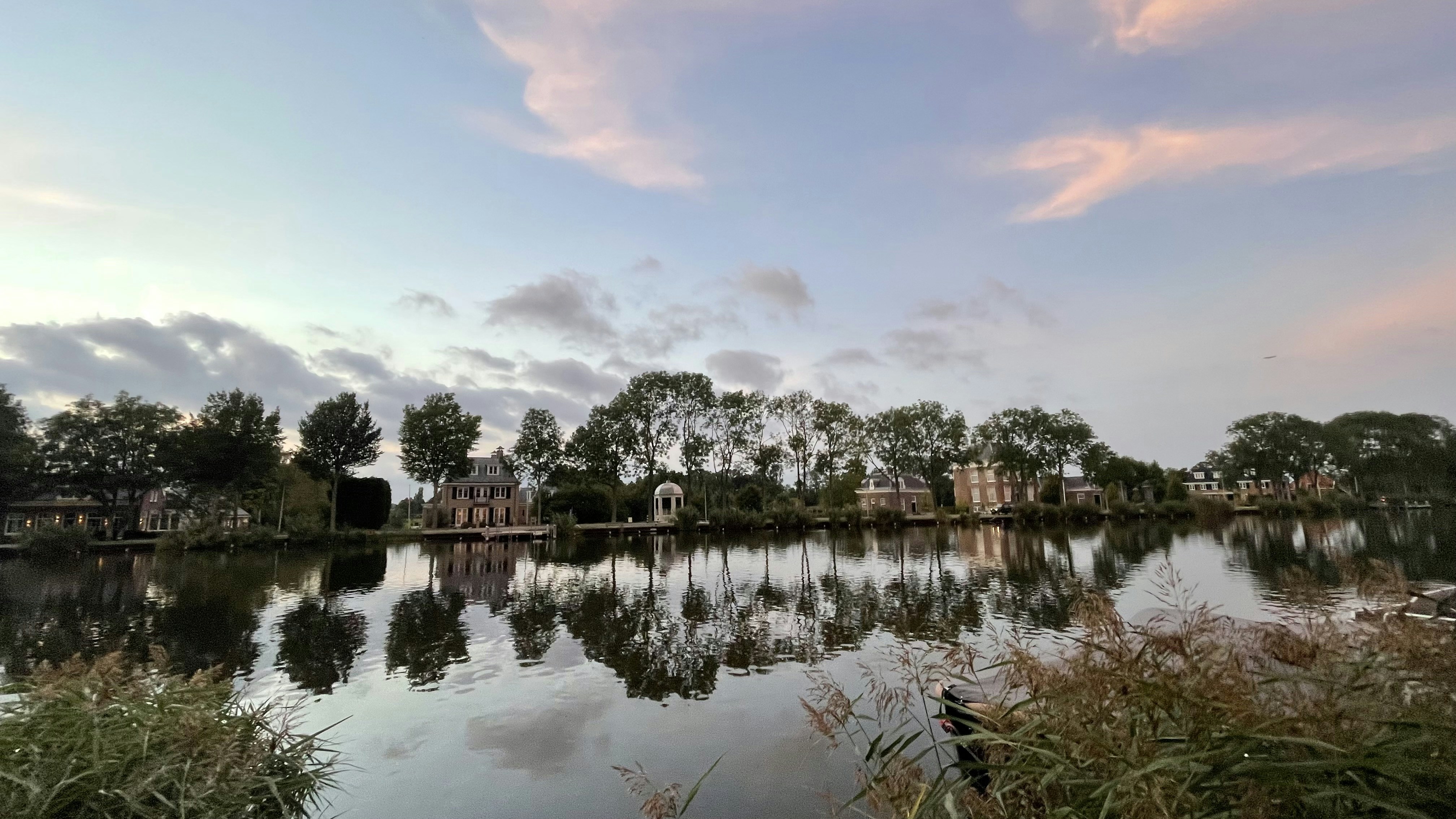 Serene lakeside scene with reflections of trees and houses under a pastel sky at dusk.