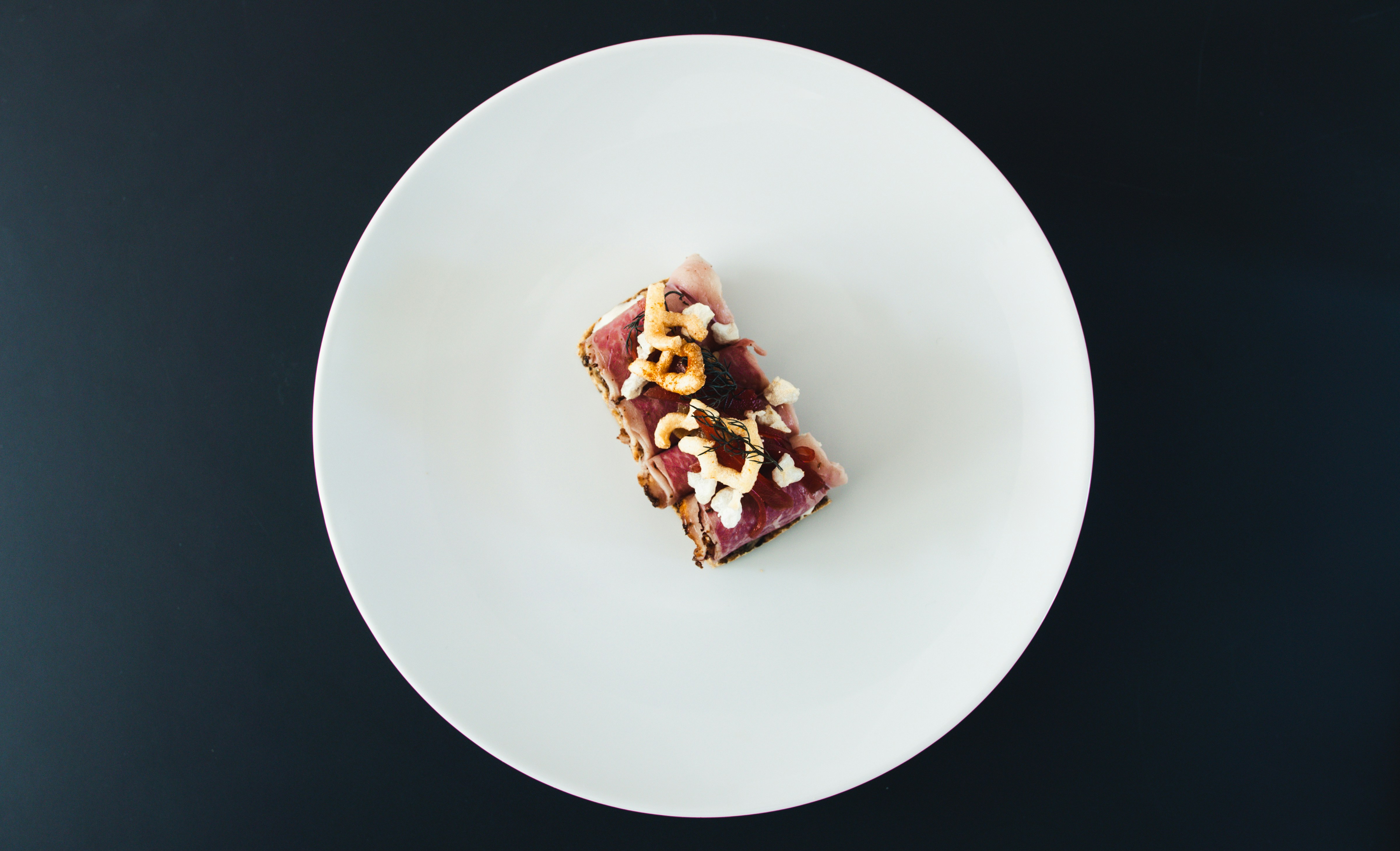 A single sushi roll adorned with toppings sits elegantly on a white plate against a dark background.