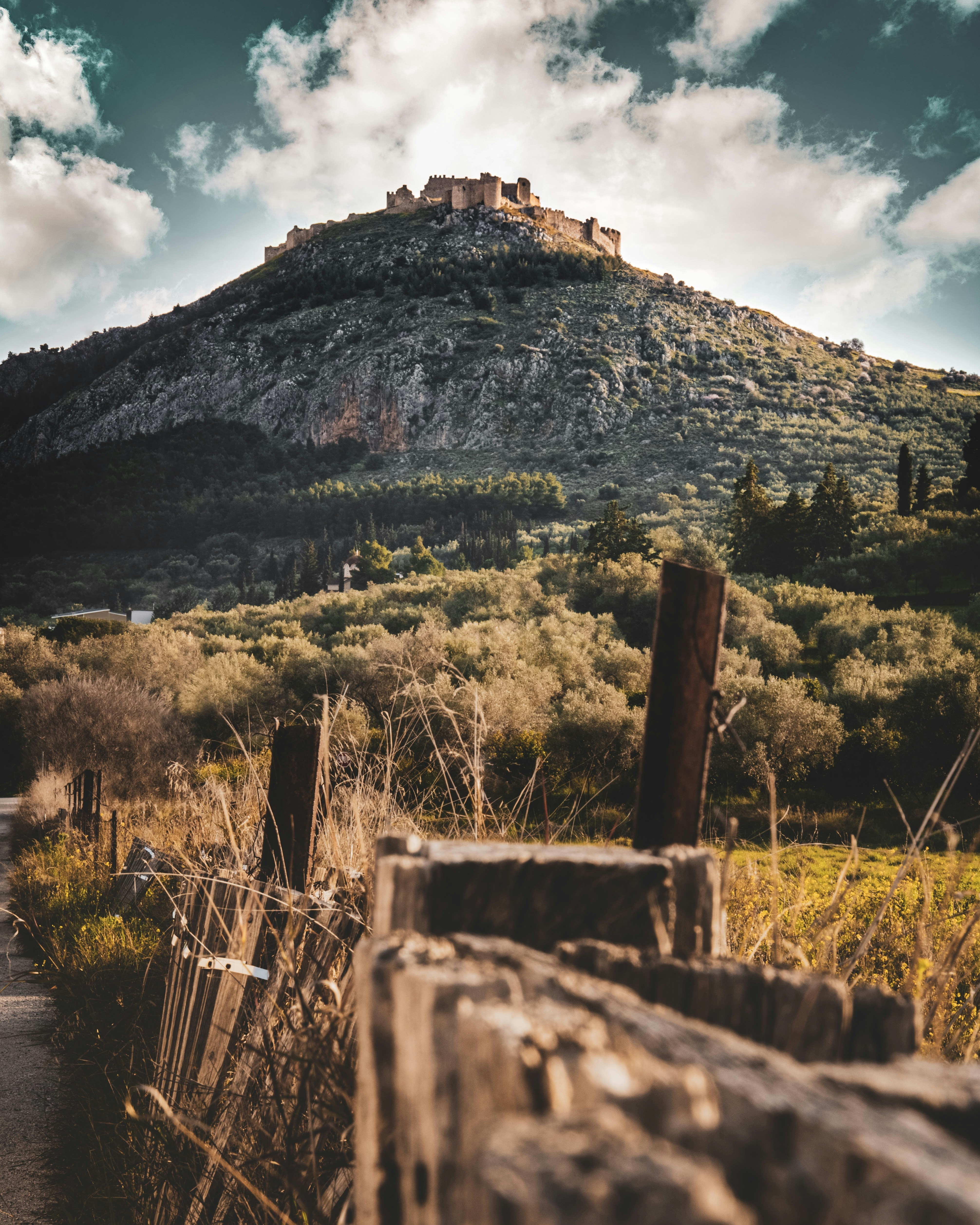 Ancient castle perched atop a verdant hill under a sky with dramatic clouds.