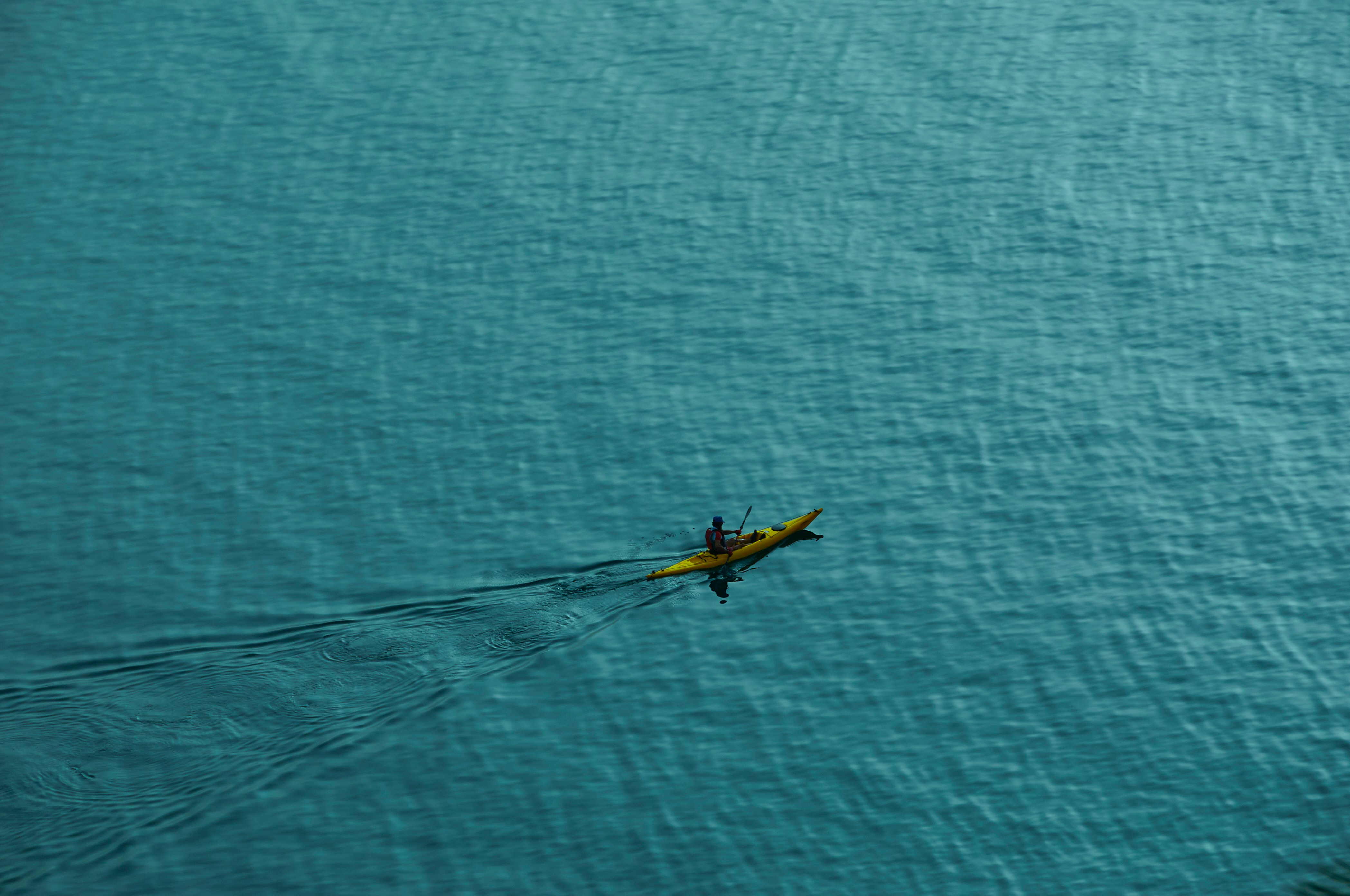 A lone kayaker glides across the tranquil blue surface of the water, leaving gentle ripples in their wake.