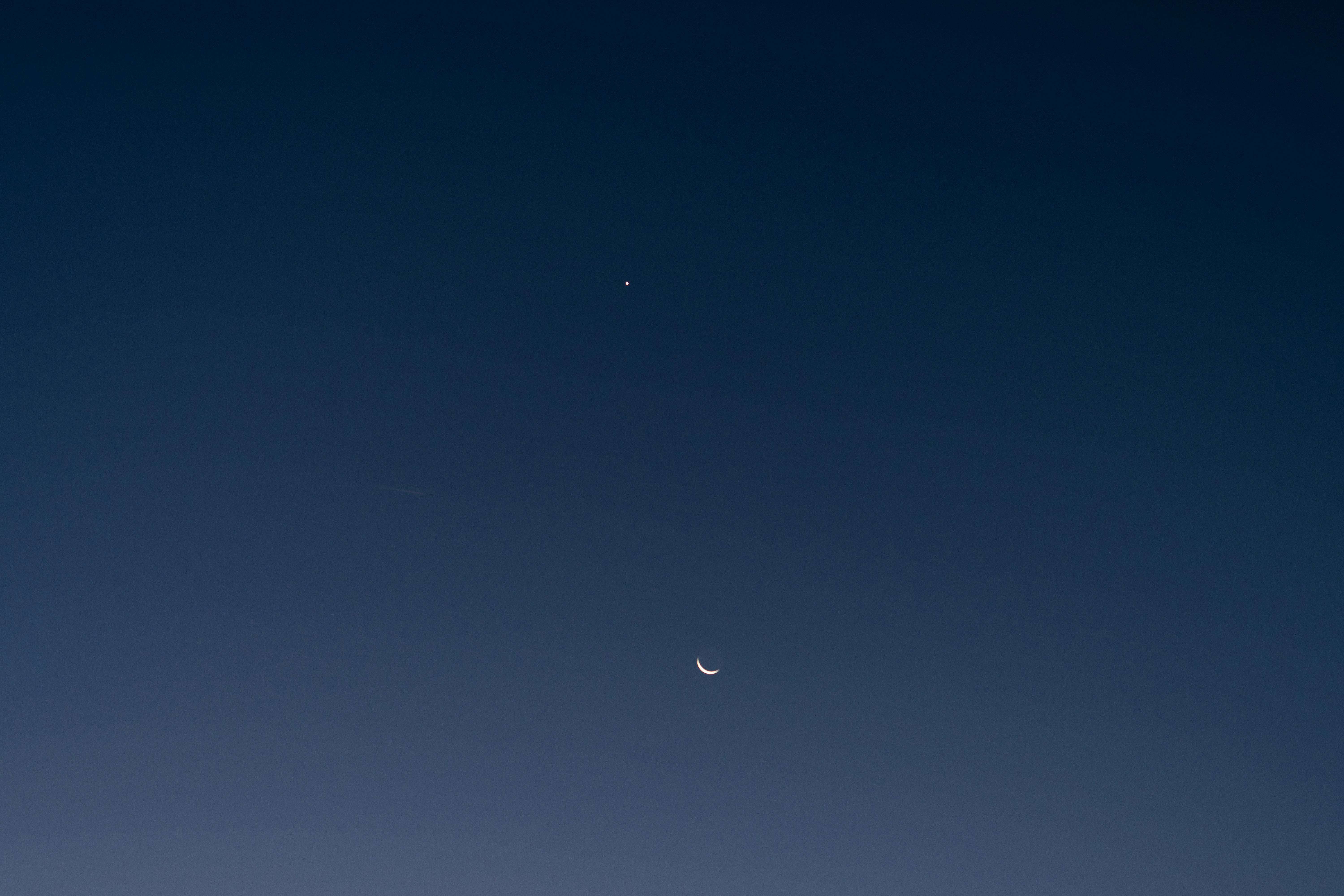 Crescent moon and Venus shine brightly in a deep blue twilight sky.