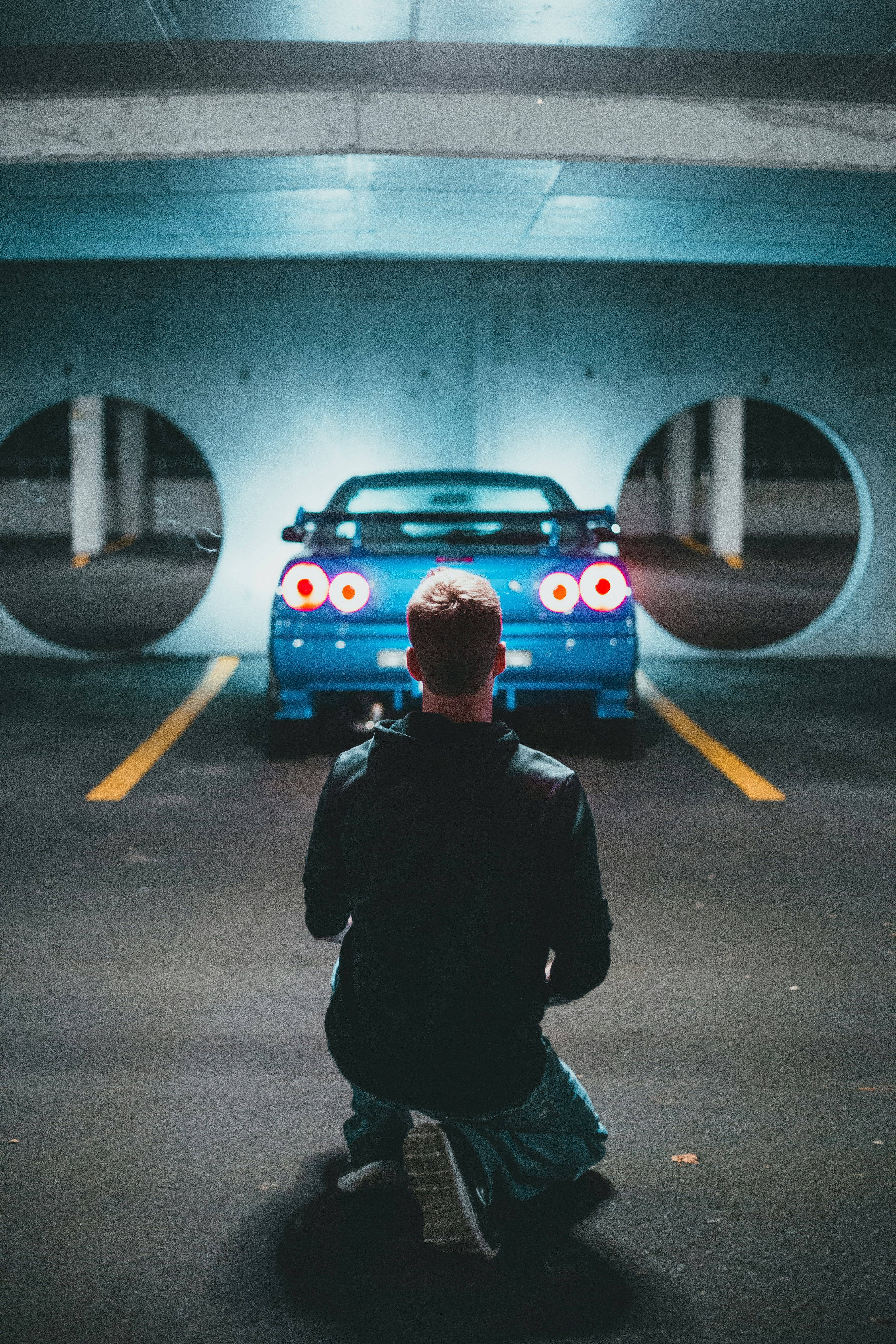 Concrete Arches and a Blue Beast: A kneeling figure faces a blue sports car in a circular-arched parking garage