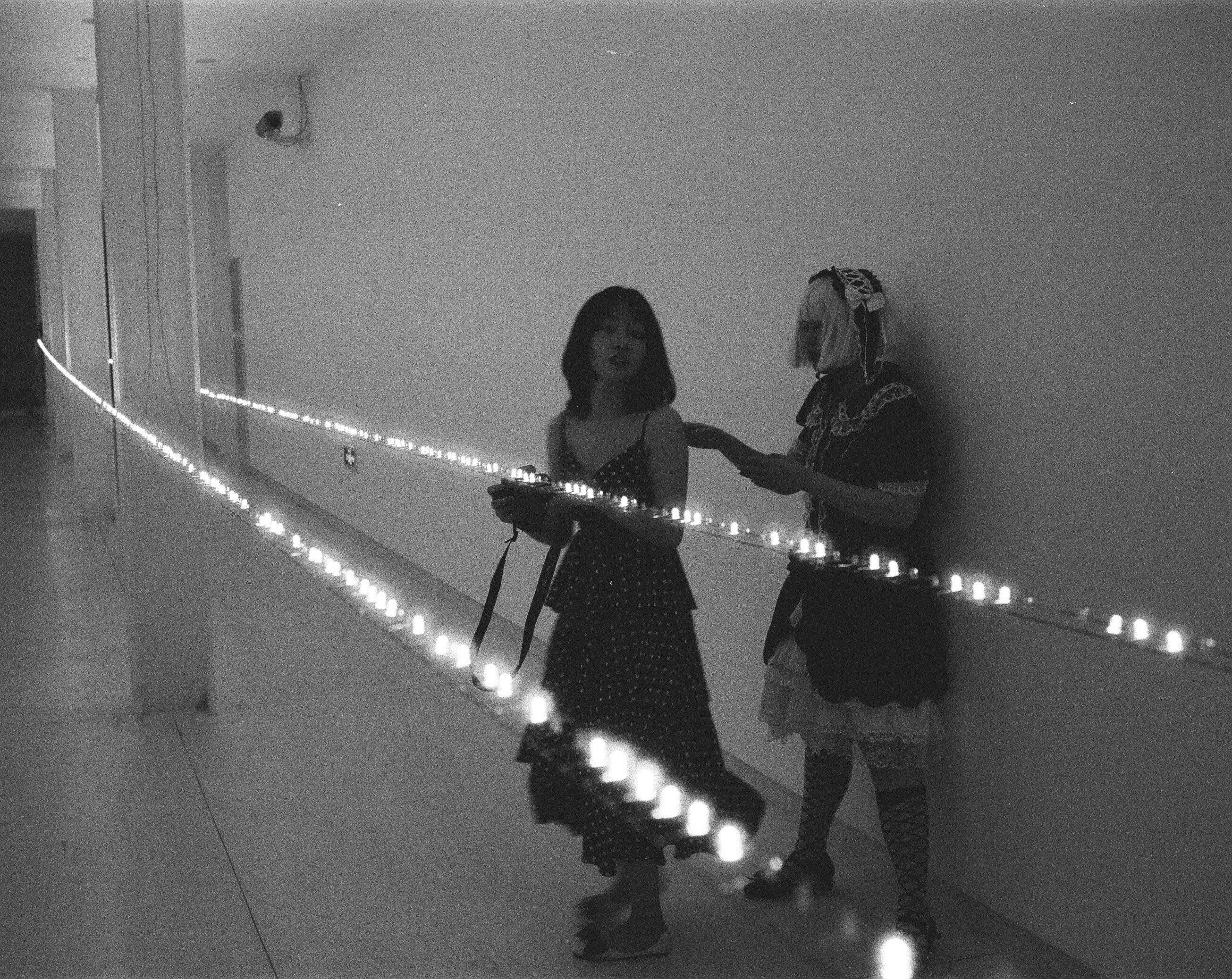 Two figures in a dim corridor share a quiet conversation beneath a line of glowing orbs
