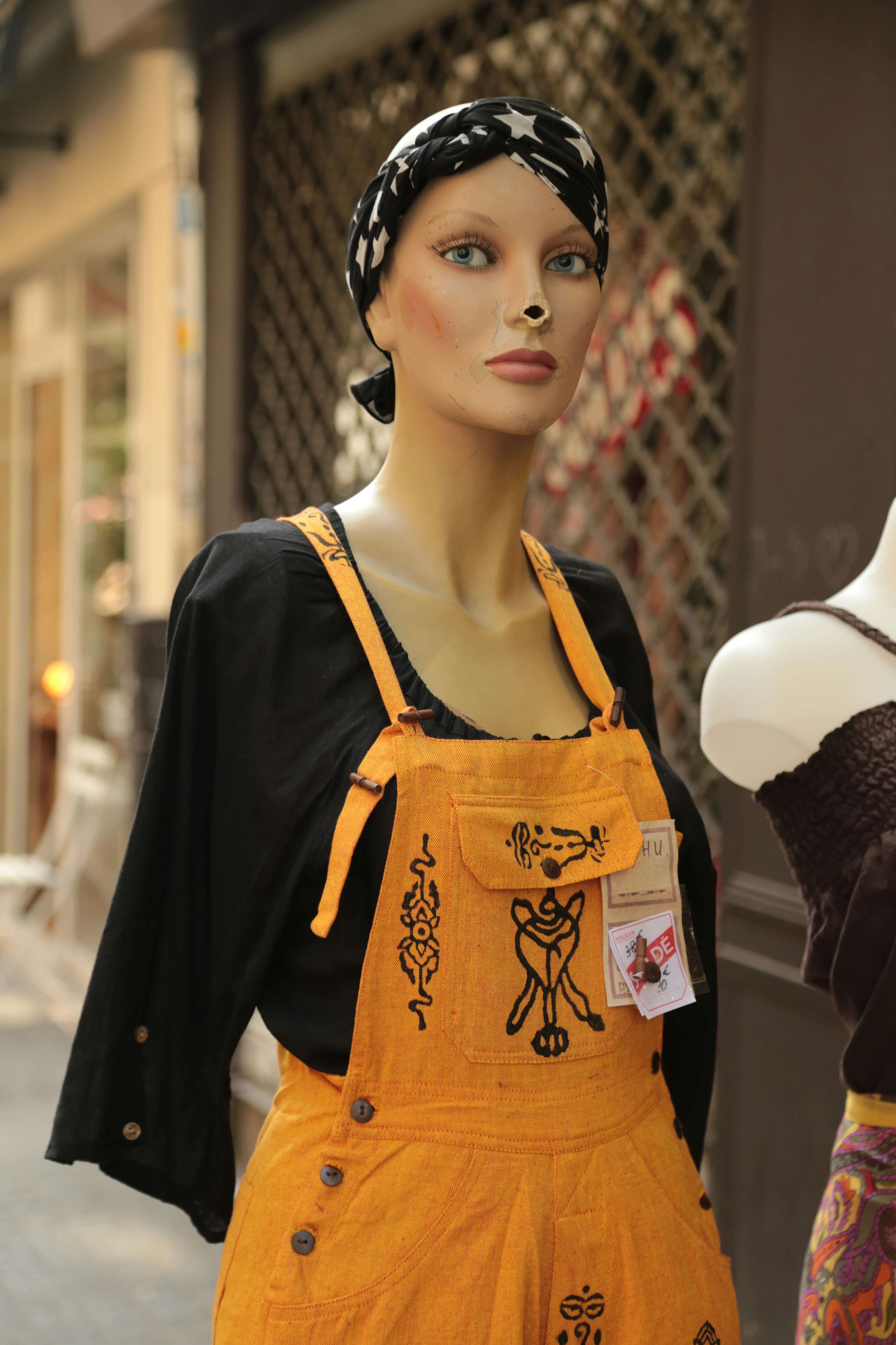 Mannequin dressed in a vibrant orange jumpsuit with intricate designs, set against a blurred urban backdrop.