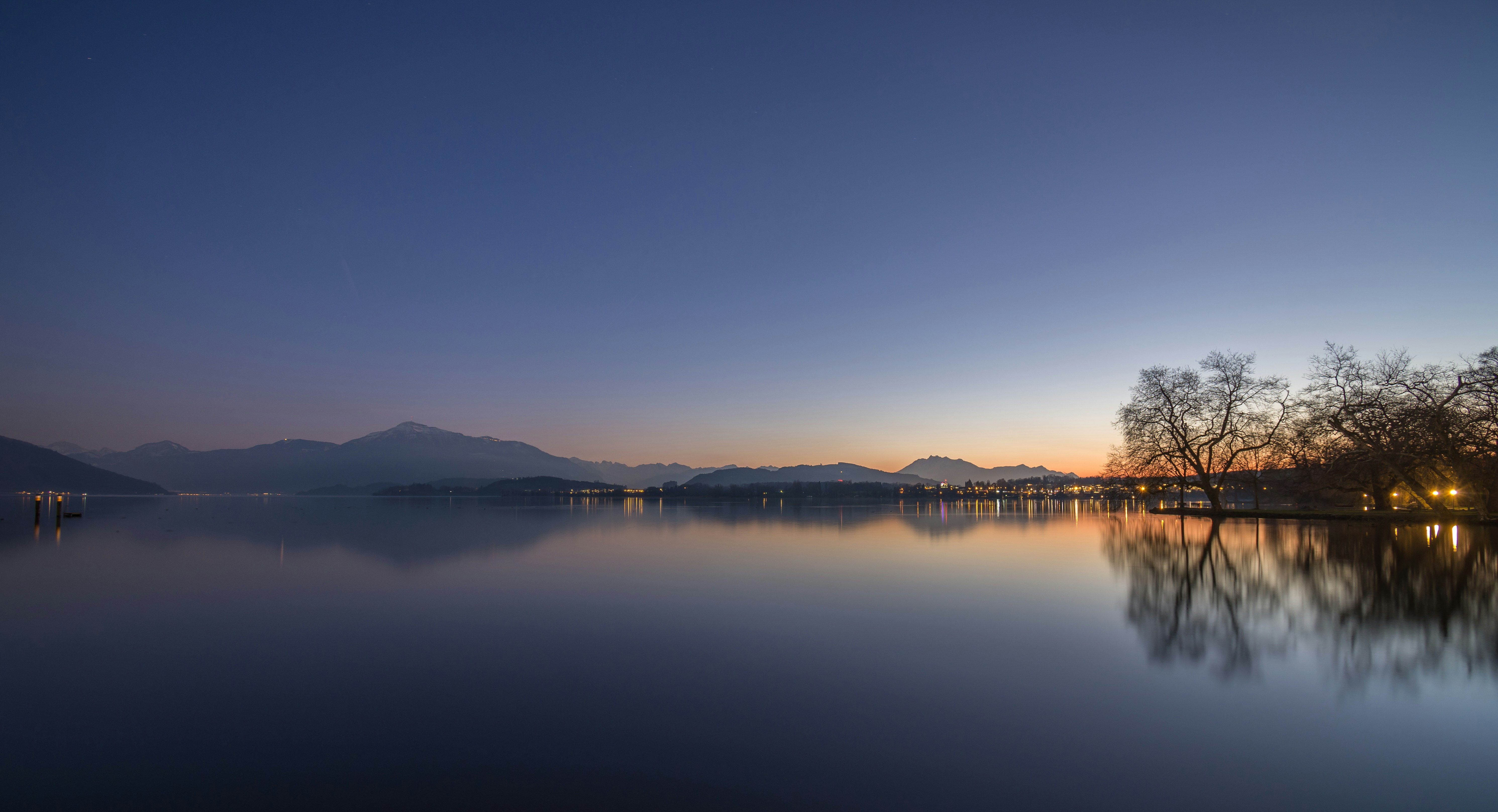 Serene twilight over Lake Zug with silhouetted trees and distant mountains.