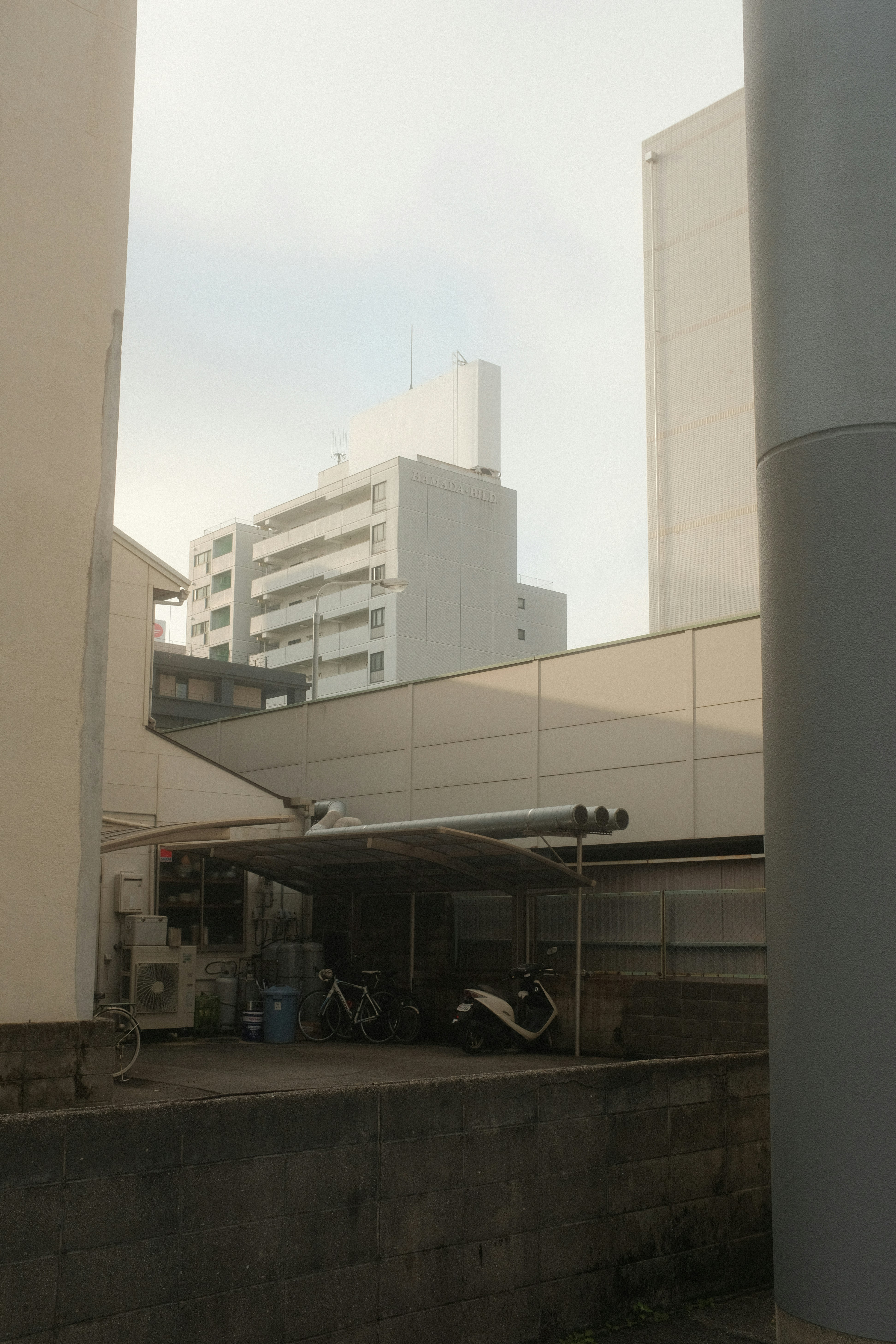 A view showcasing the juxtaposition of modern architecture and everyday urban elements, featuring buildings, bicycles, and a scooter. 
