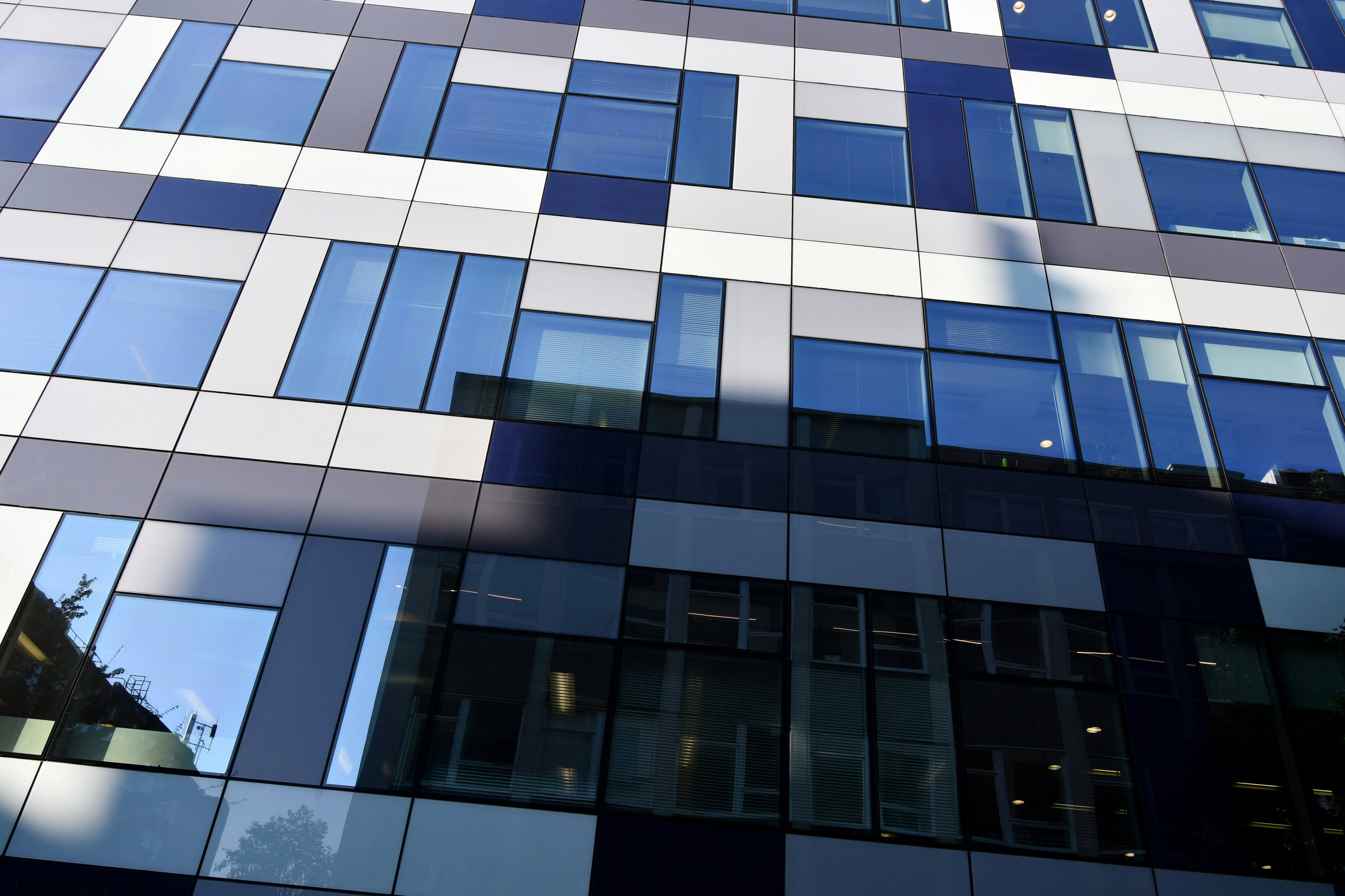 Modern building facade featuring a mosaic of glass and panel sections, reflecting light patterns and urban surroundings.