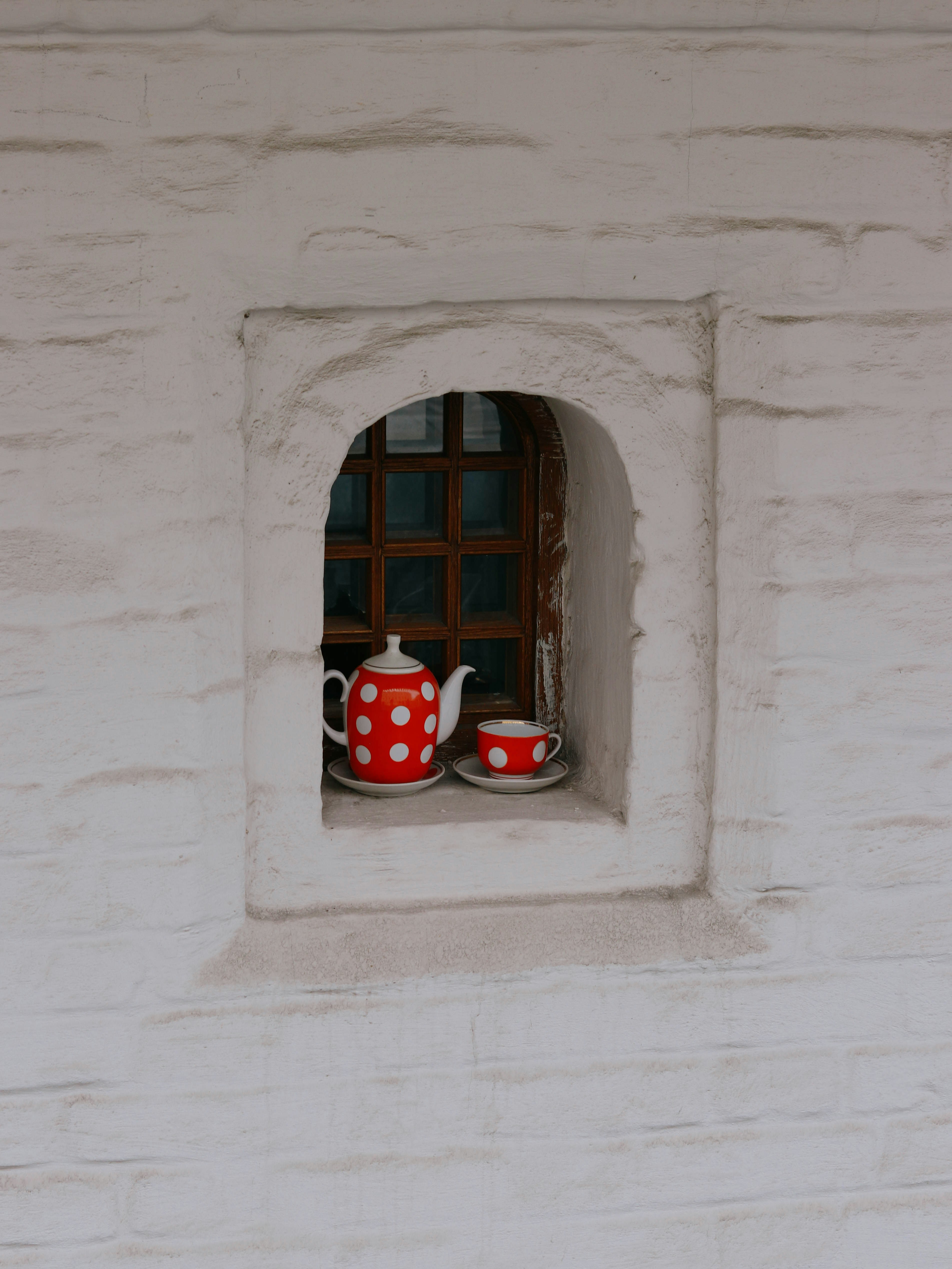 a red and white tea pot and two cups in a window