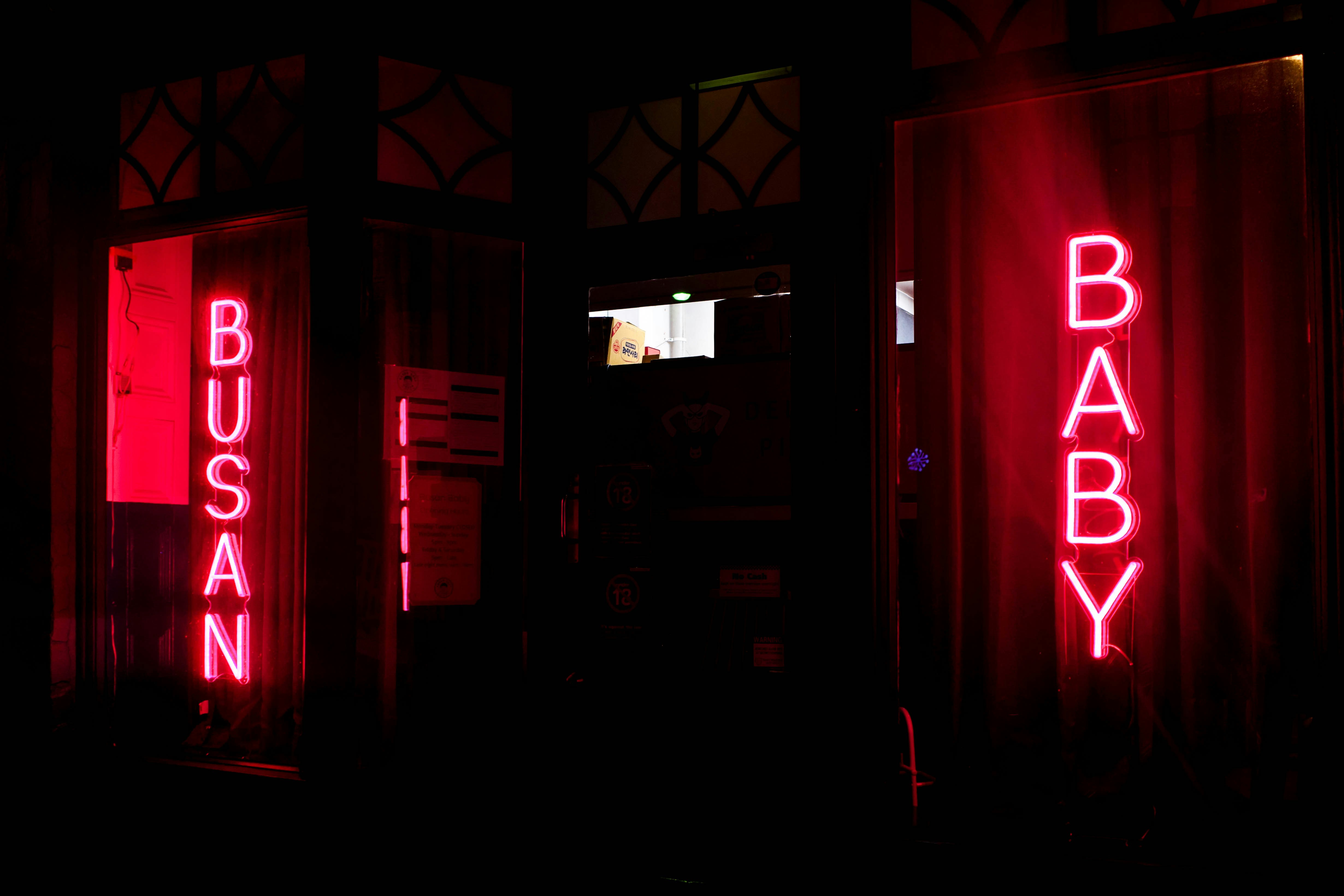 Crimson Neon Gate: Busan and Baby Silhouettes in a Night Entrance