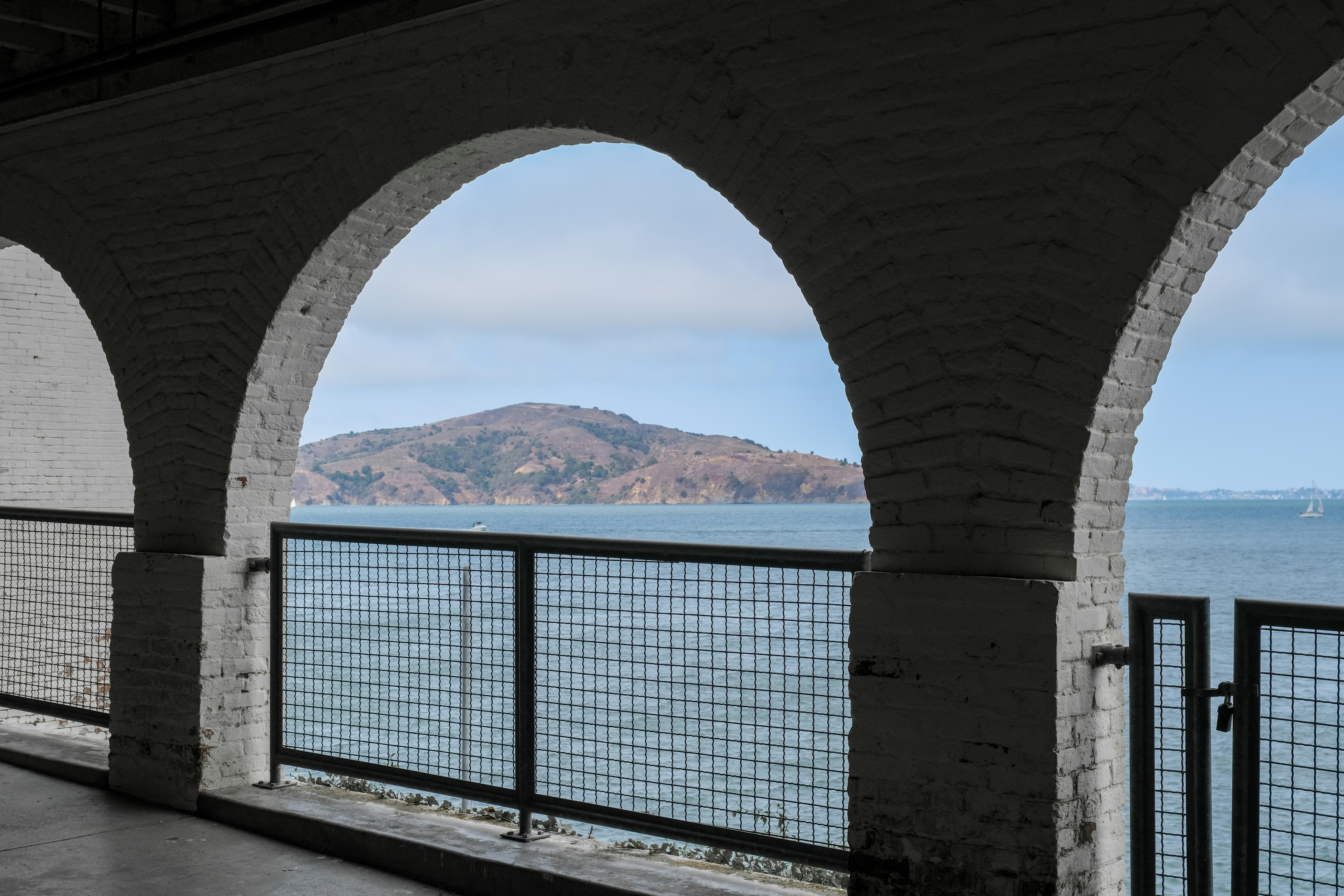 Arched openings reveal a tranquil seascape with a distant hill, creating a harmonious blend of architecture and nature.