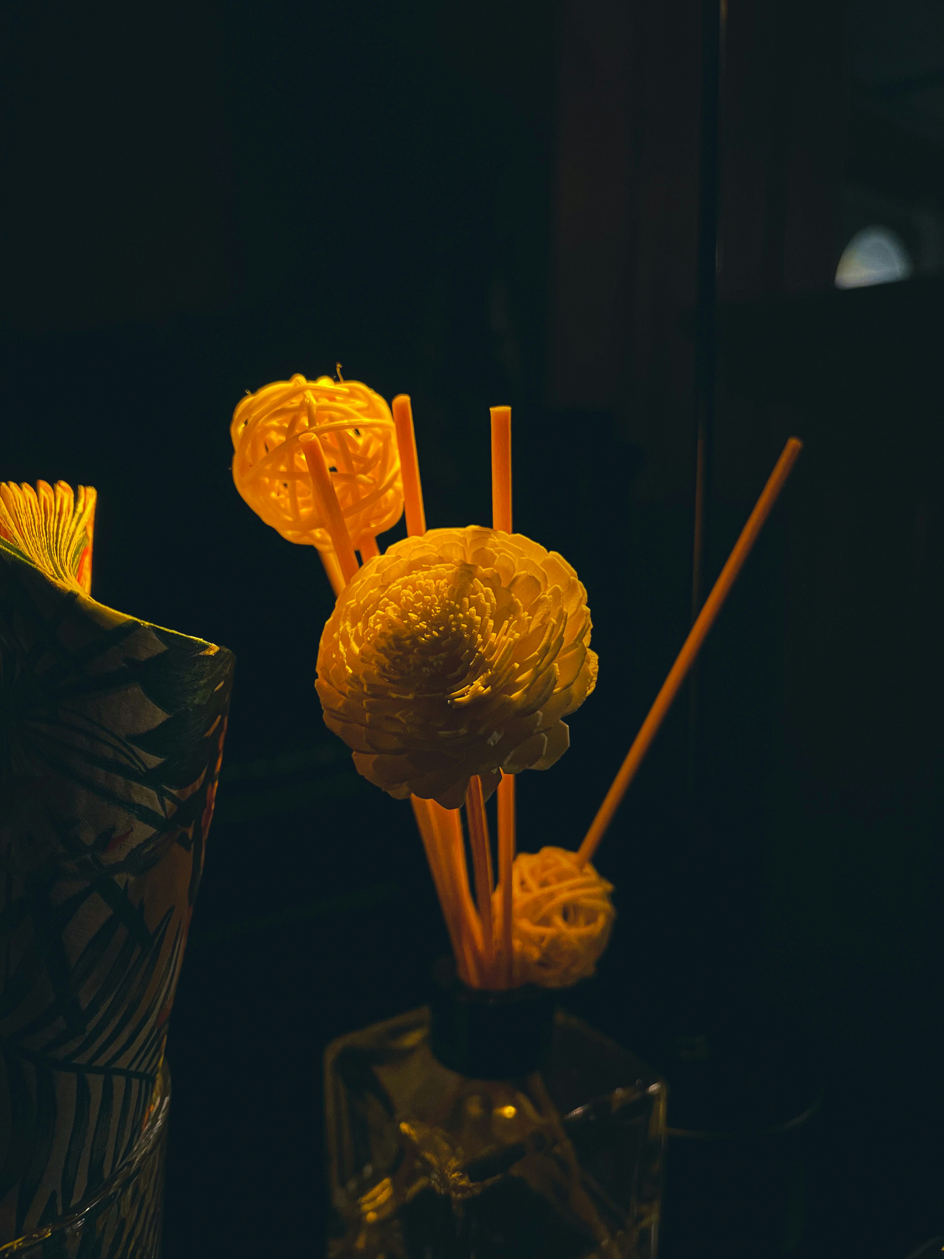 Delicate yellow flowers arranged in a dark setting, highlighted by soft lighting. The composition emphasizes texture and form.