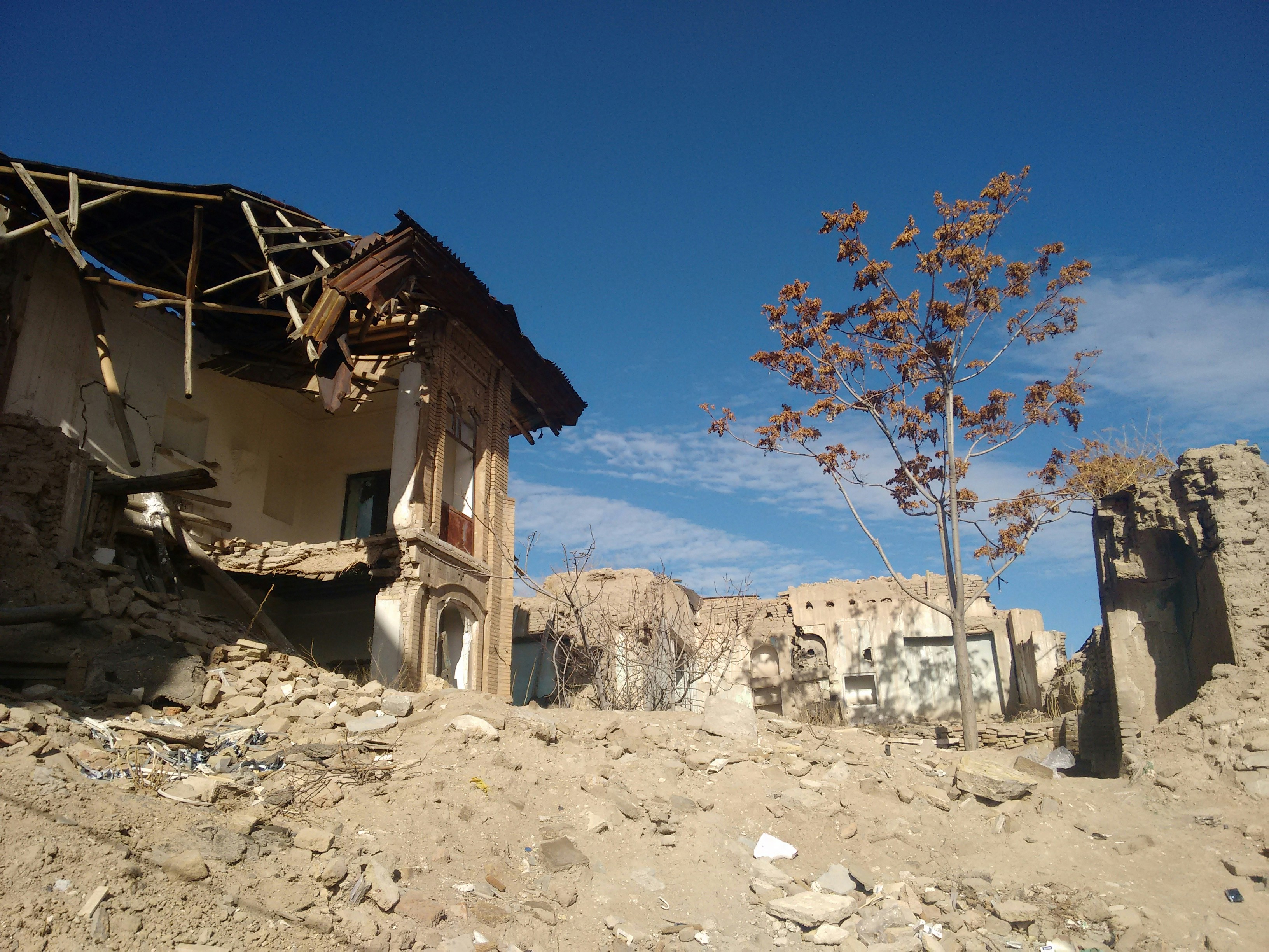 Crumbling building and barren tree under a clear blue sky in a deserted landscape.