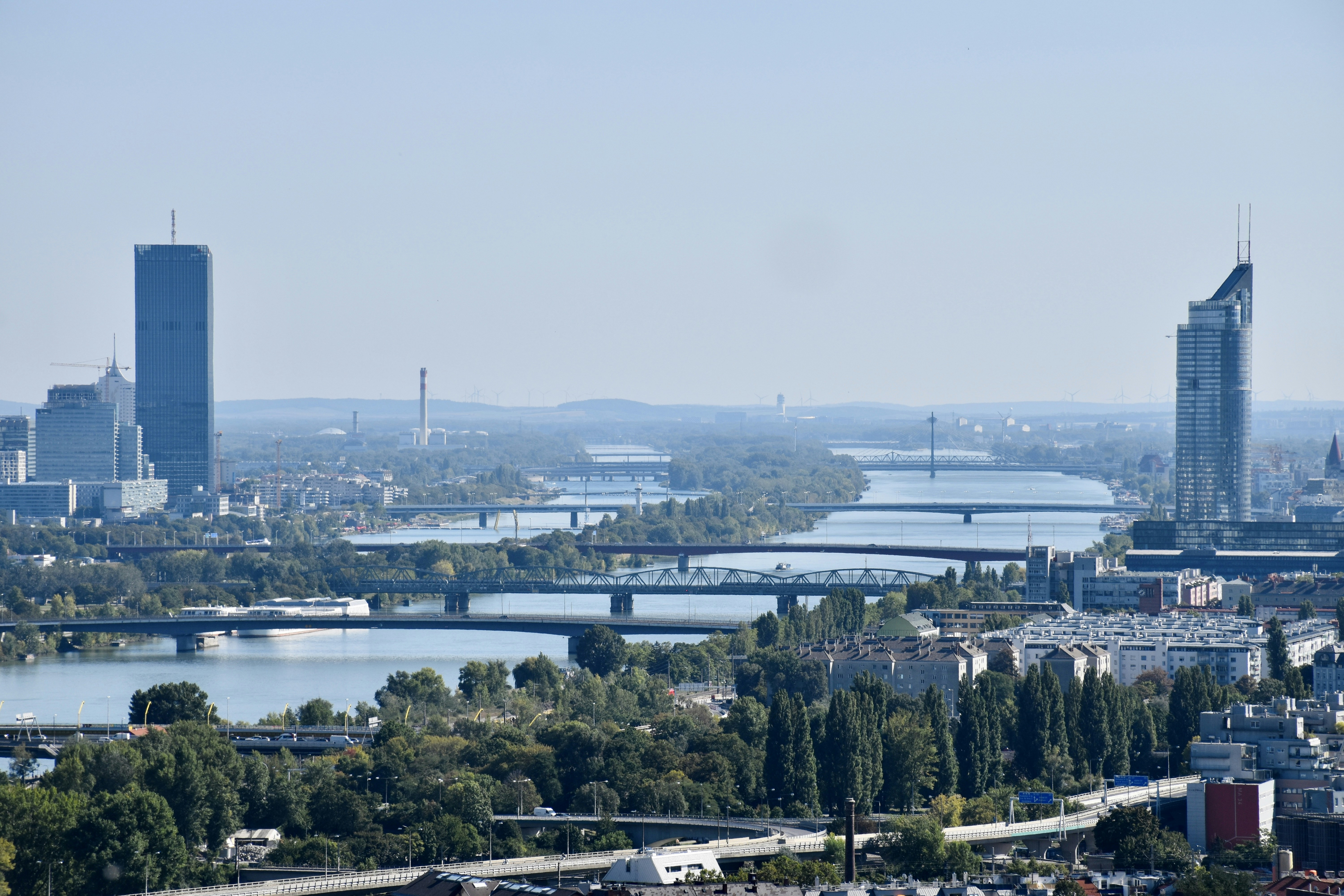 A panoramic view of a city skyline featuring modern architecture along a winding river, framed by lush greenery and bridges. The scene captures the harmonious blend of nature and urban life.