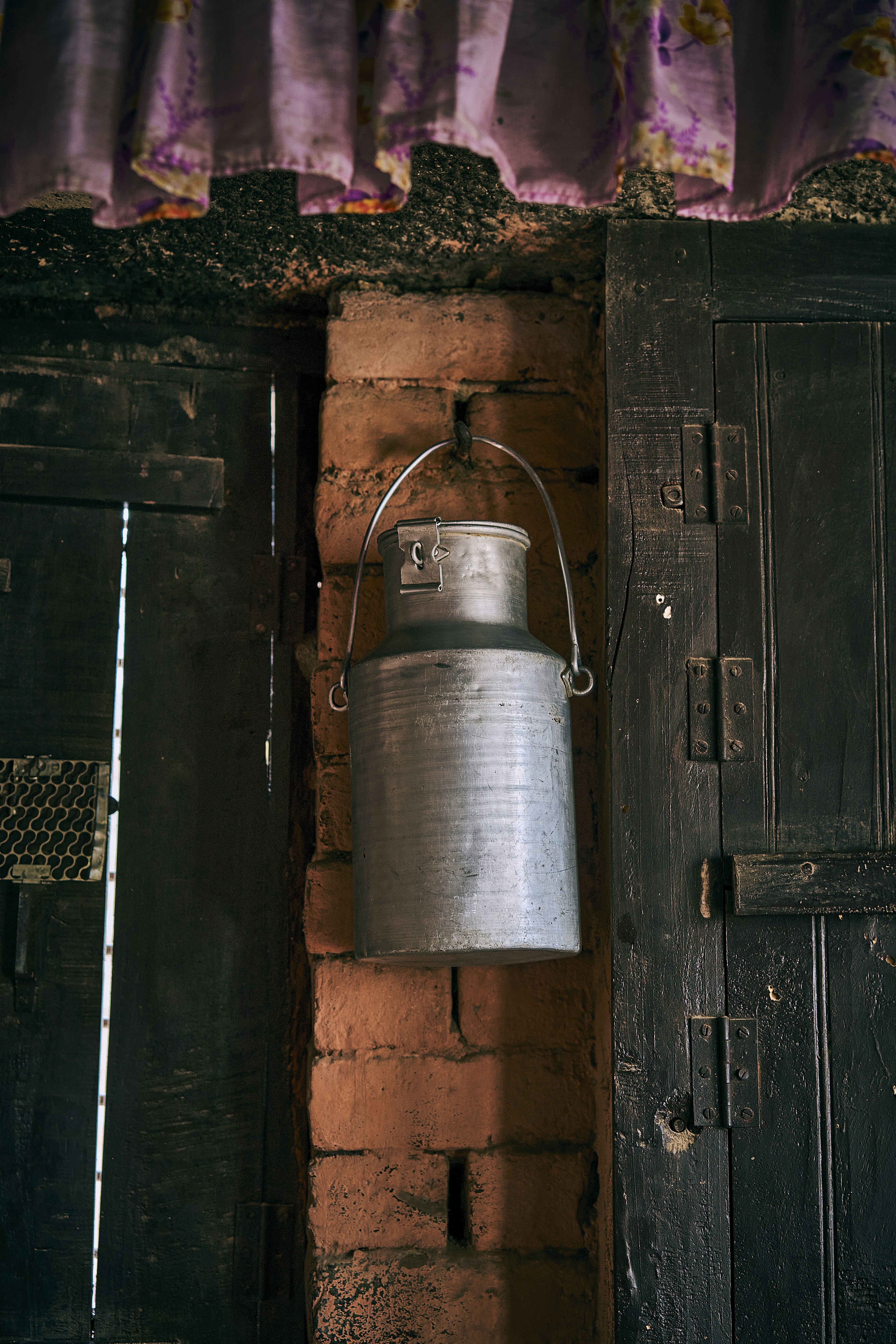 Silver Milk Can Framed by Weathered Doors in a Brick-Walled Rustic Hallway
