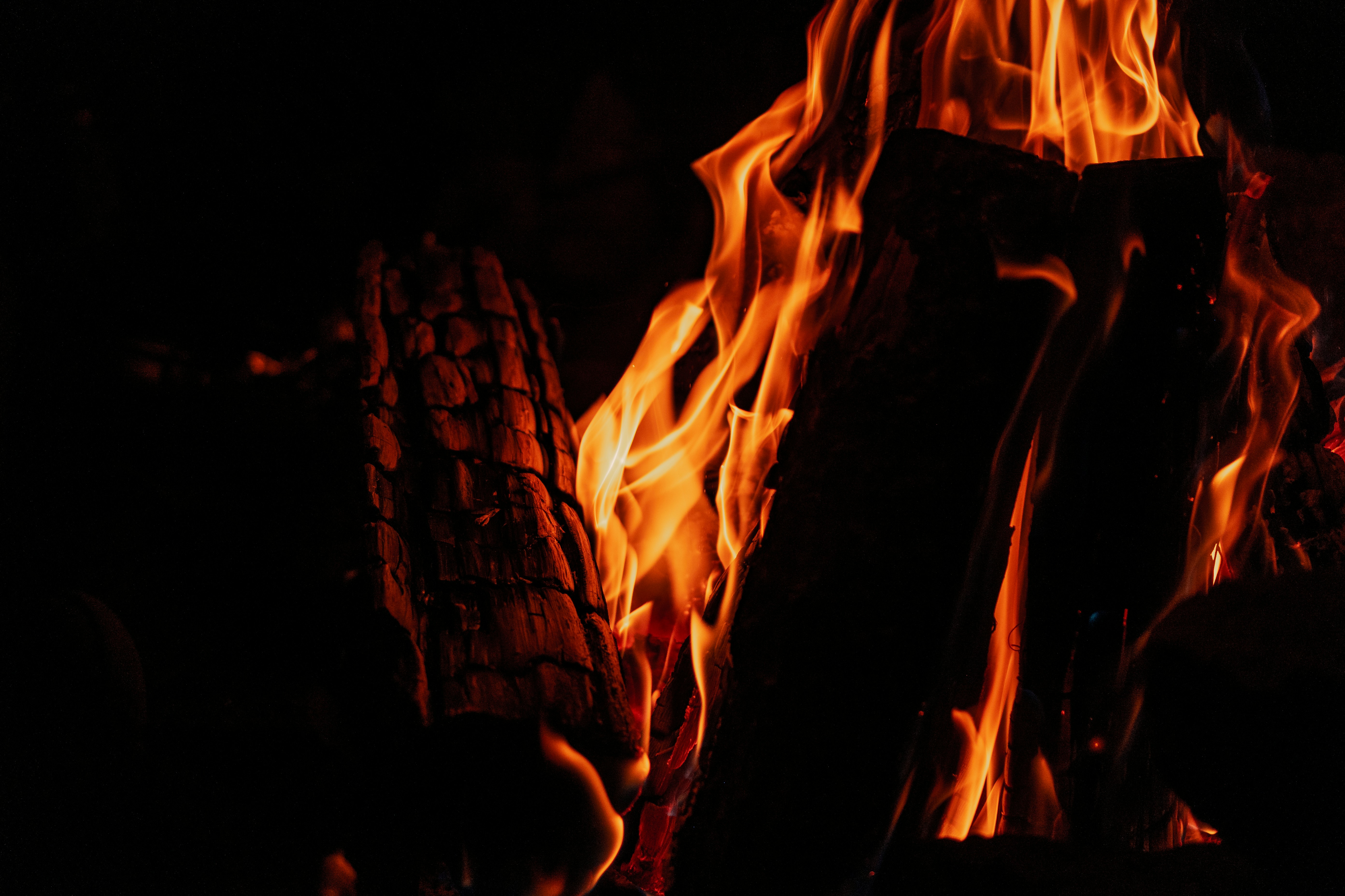 Flames flicker and twist around charred logs in a cozy fire, creating a warm and inviting atmosphere.