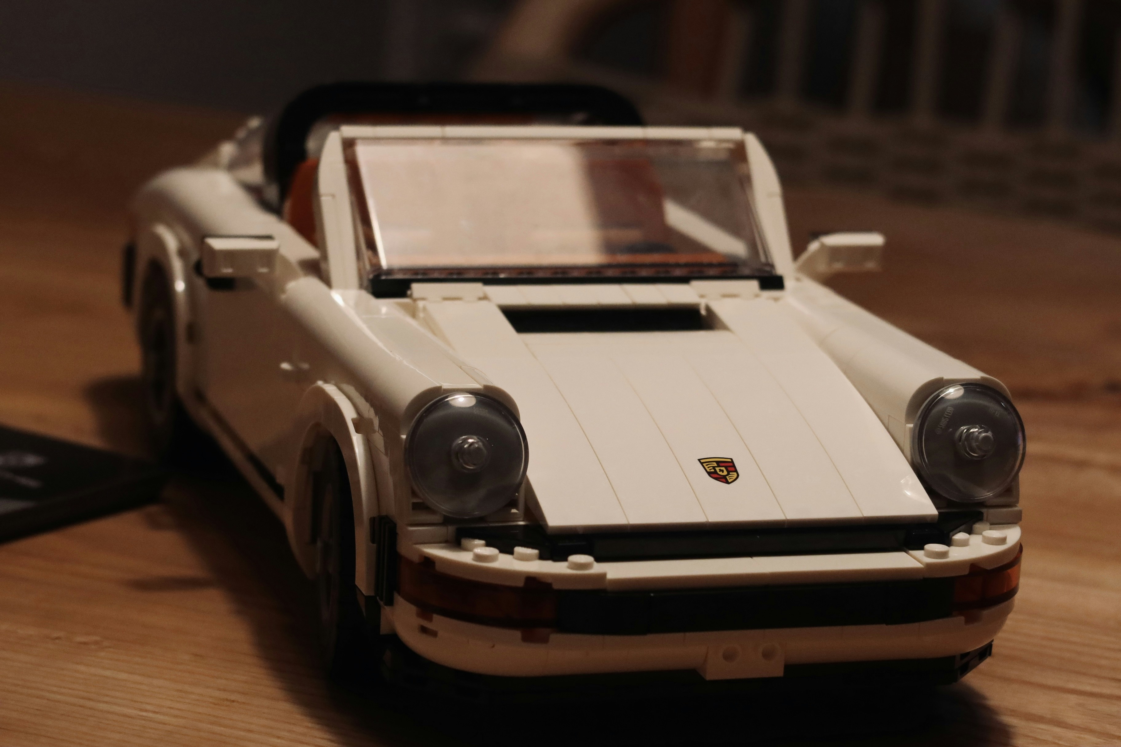 White LEGO Porsche sports car model sits on a wooden surface, photographed in warm indoor light.