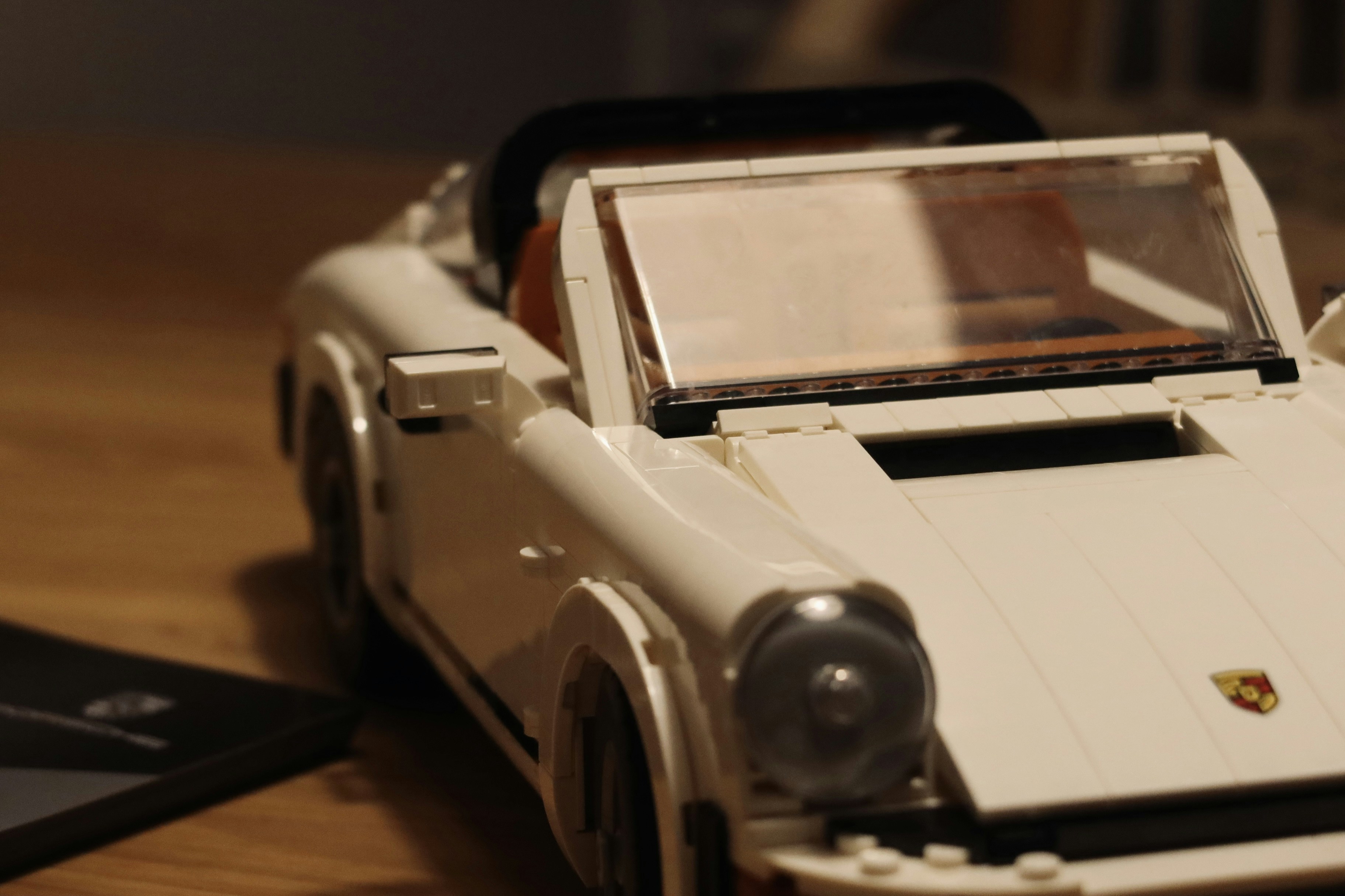 Detailed model of a white convertible sports car, showcasing intricate design elements and craftsmanship. Set against a wooden surface, it highlights the charm of automotive artistry.
