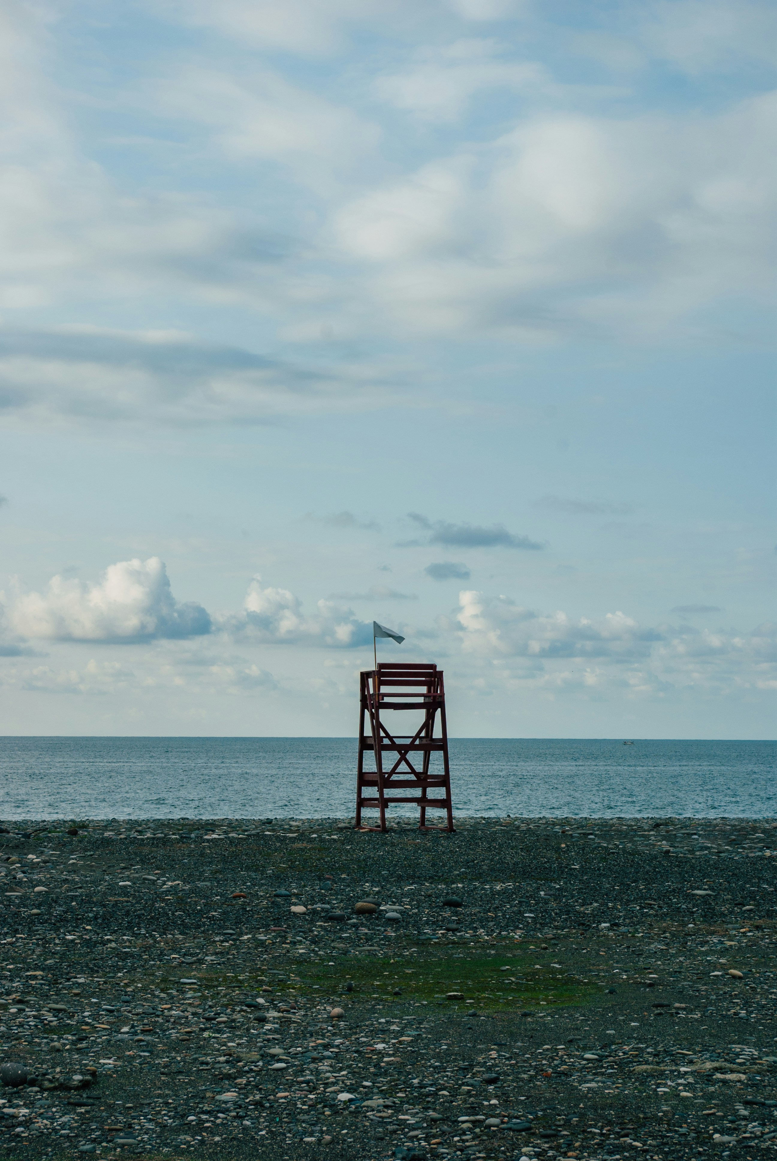 Solitary Lifeguard Chair Framed by Pebbles, Sea, and Sky