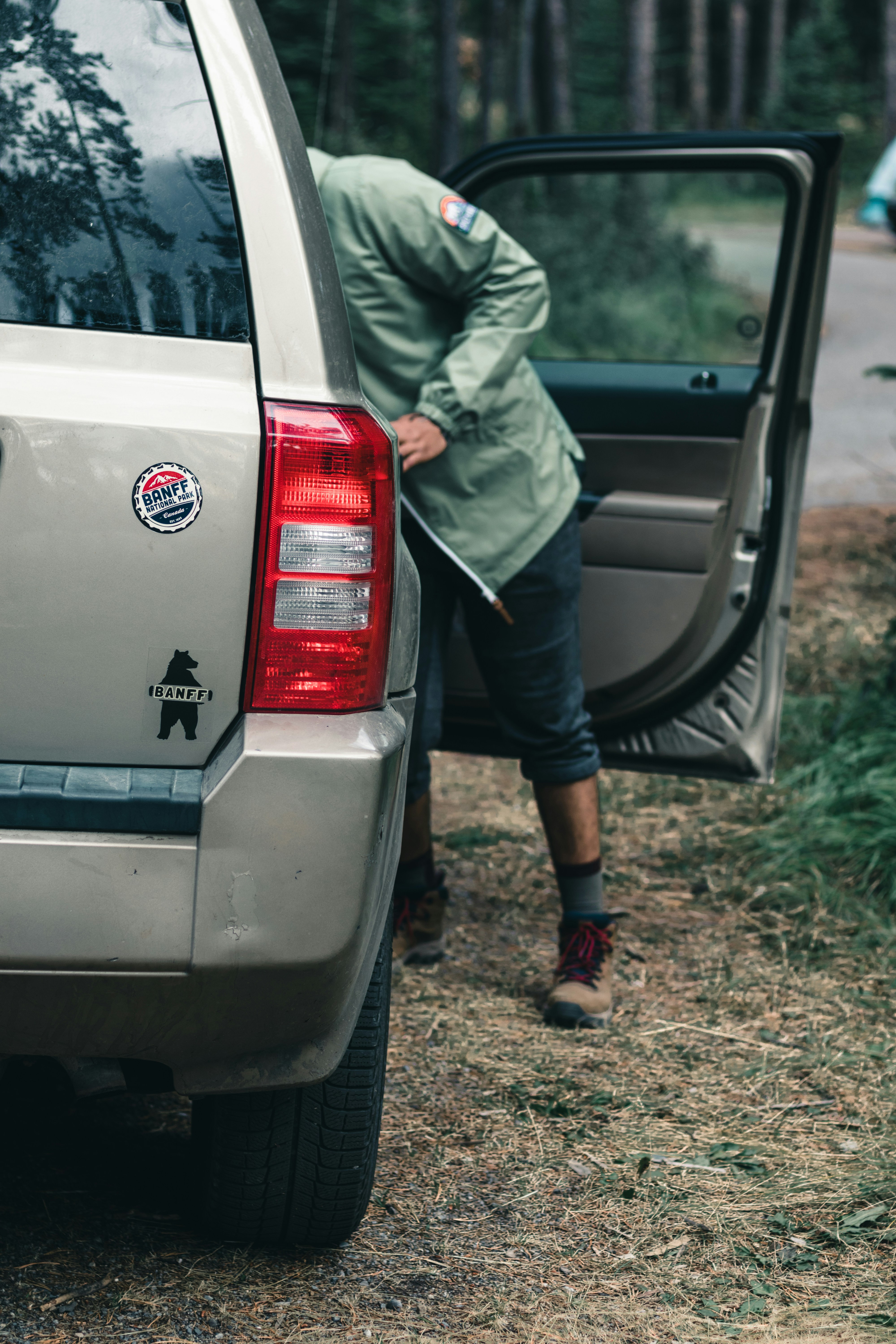 Trailhead Task: A hiker tending to an open SUV at the forest’s edge