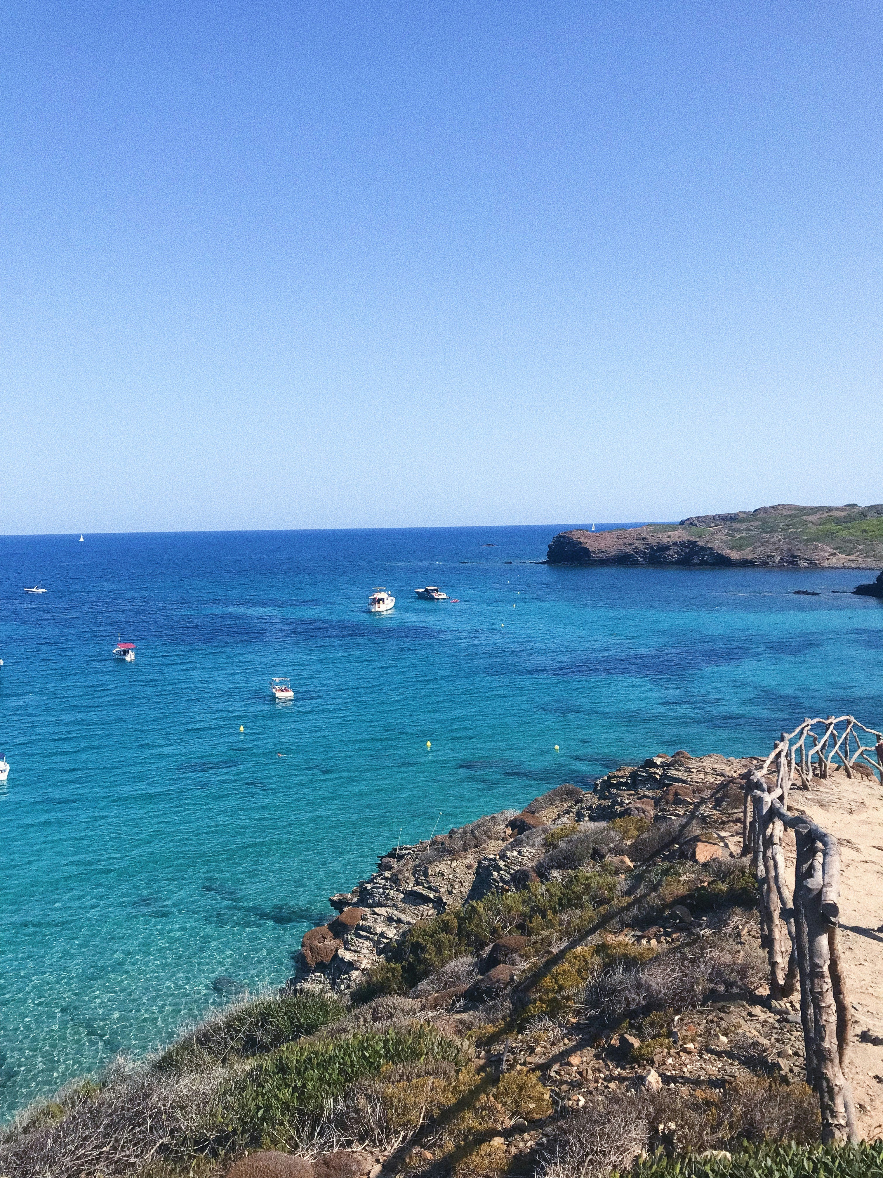 A beach in Menorca, close to a stunning lighthouse. In order to get there one must walk for quite a while but it is all worth it. | a view of a beach with boats in the water