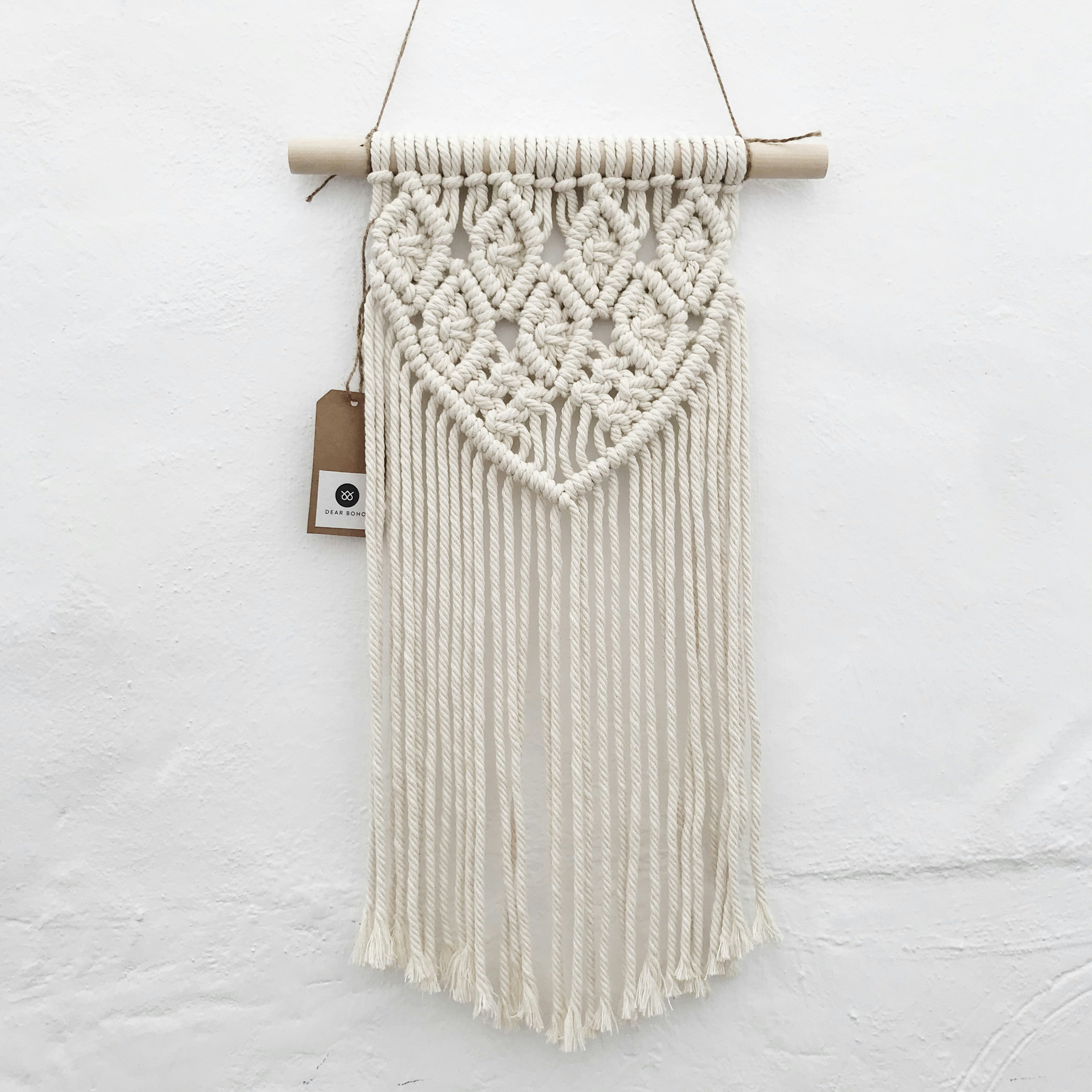 Intricate macramé wall hanging featuring a heart-shaped design with cascading fringes, elegantly displayed against a textured white background.