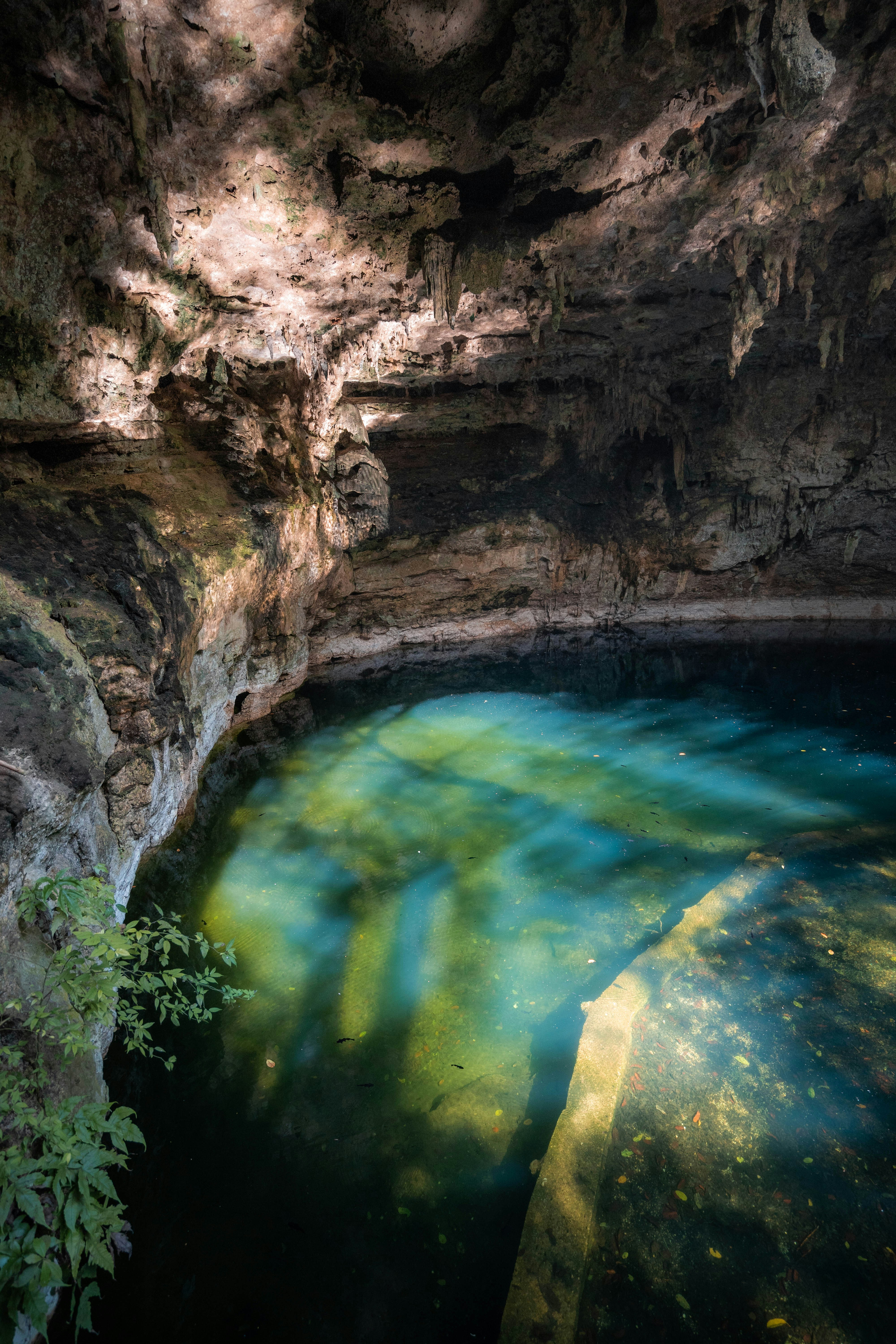 Crystal-clear water reflecting the intricate patterns of light and shadow from the rocky cave above. The serene atmosphere invites exploration.
