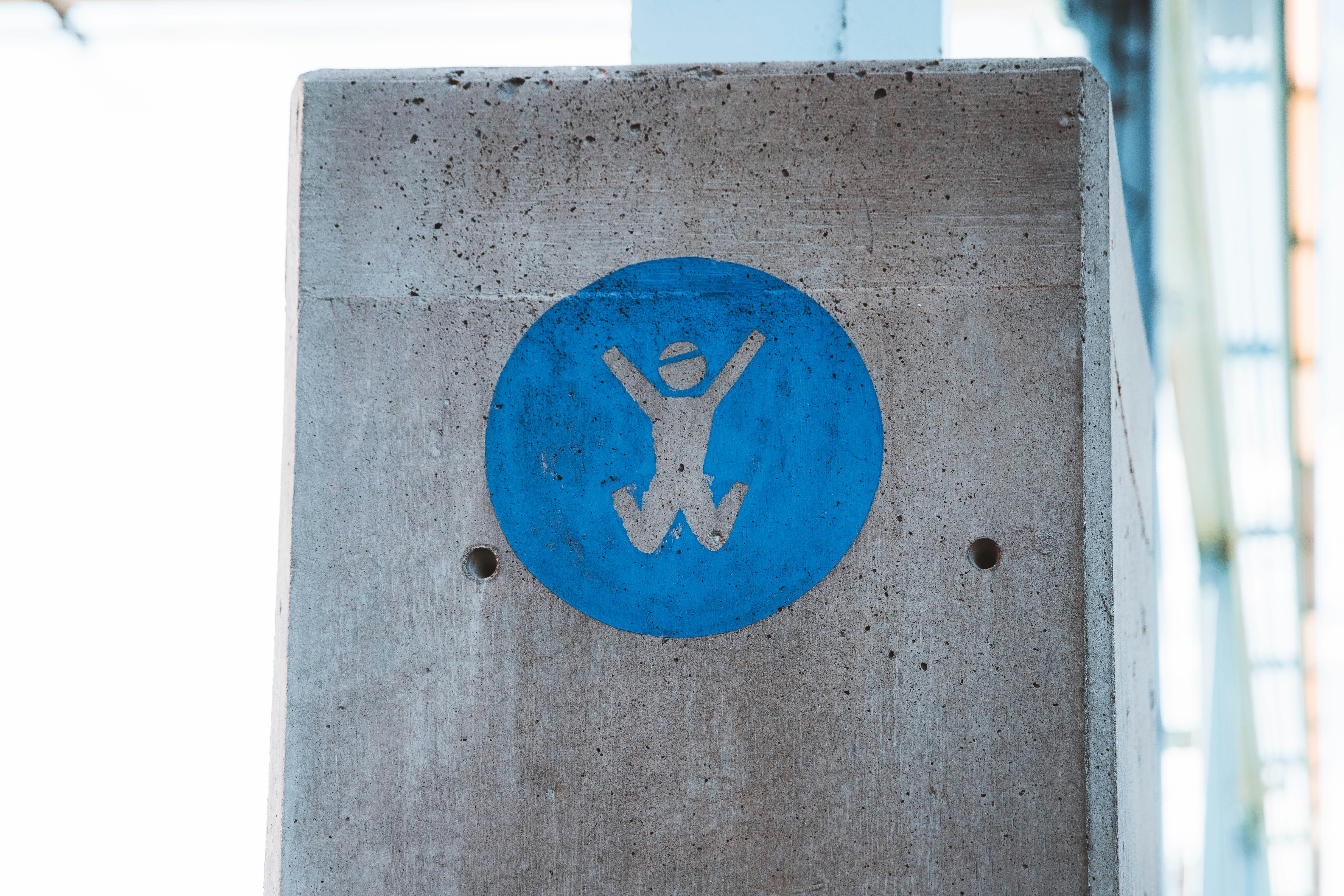Blue Circle of Safety: Jumping Figure Sign on Weathered Concrete Pillar