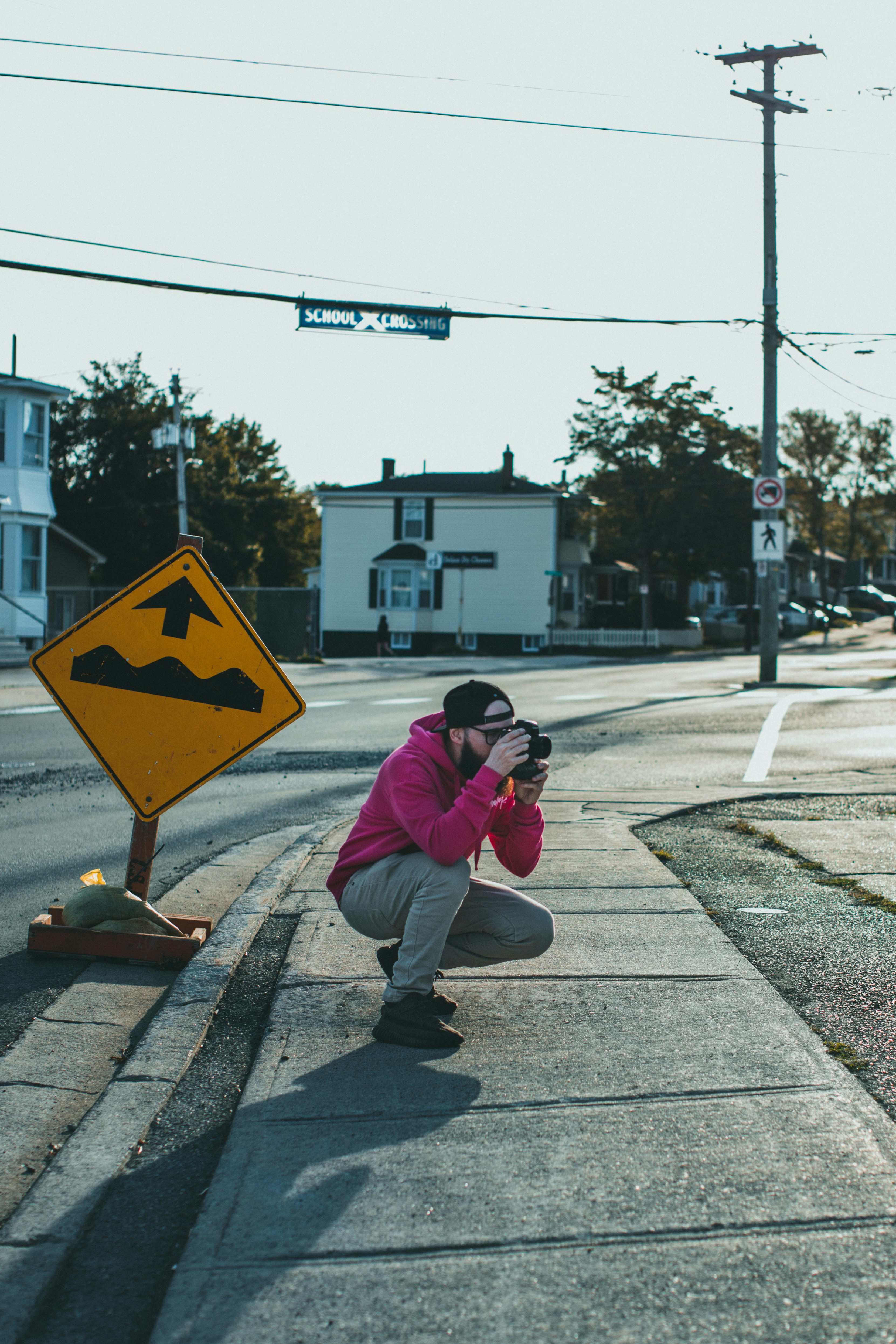 Curbside Portrait: A photographer in a pink hoodie kneels to frame street life