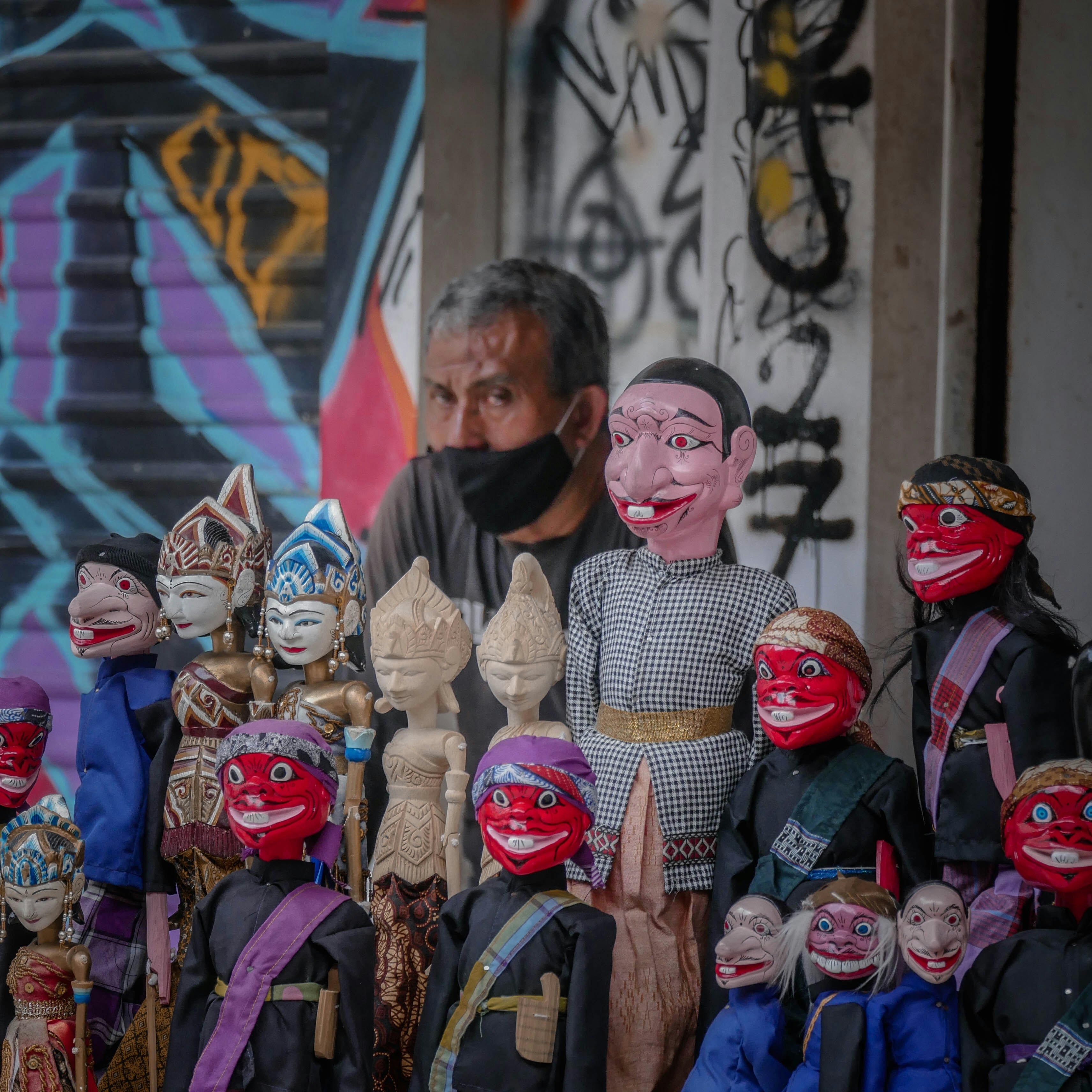 A vendor showcases intricately crafted puppets, each with vibrant expressions, against a backdrop of colorful street art.