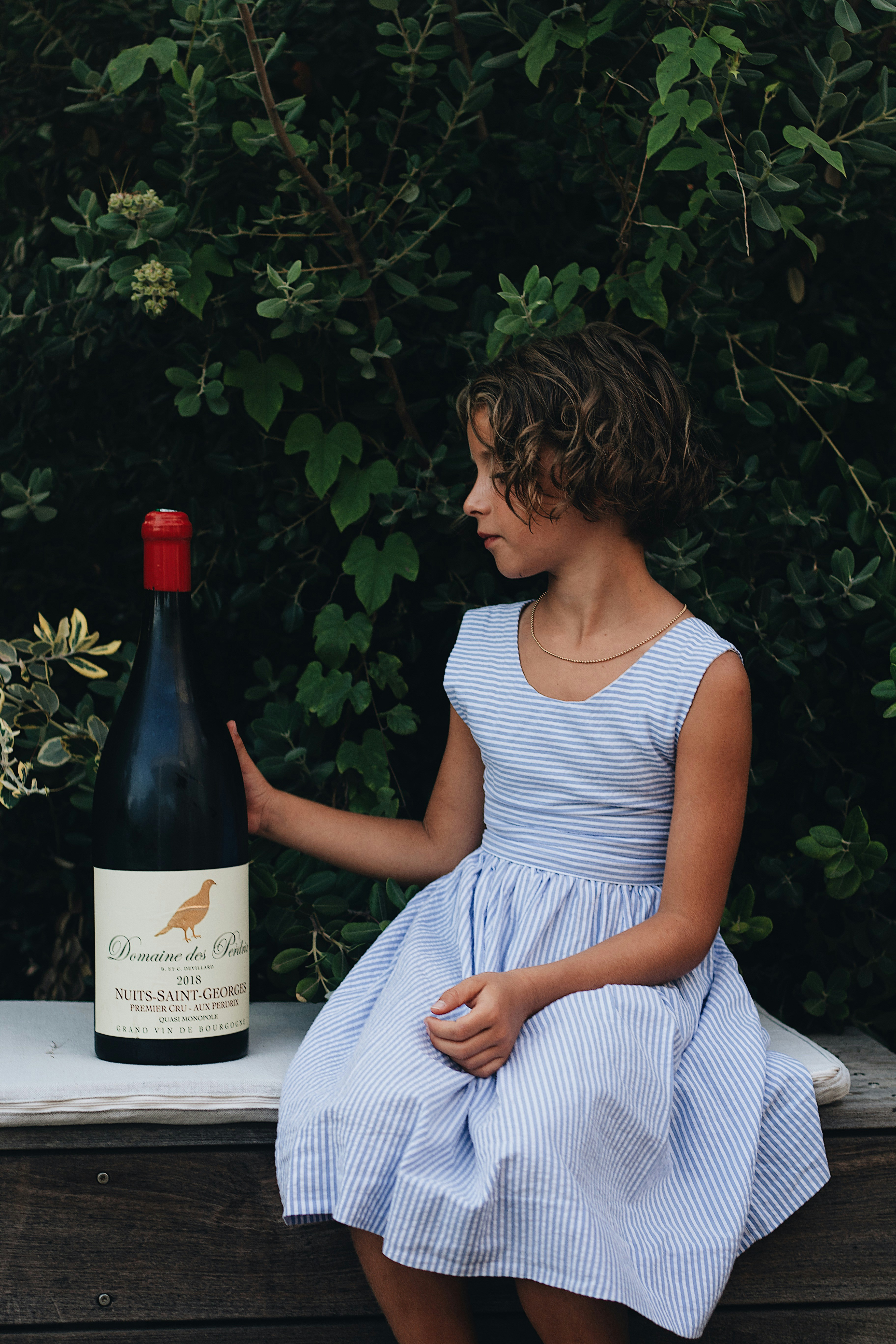 a little girl sitting next to a bottle of wine