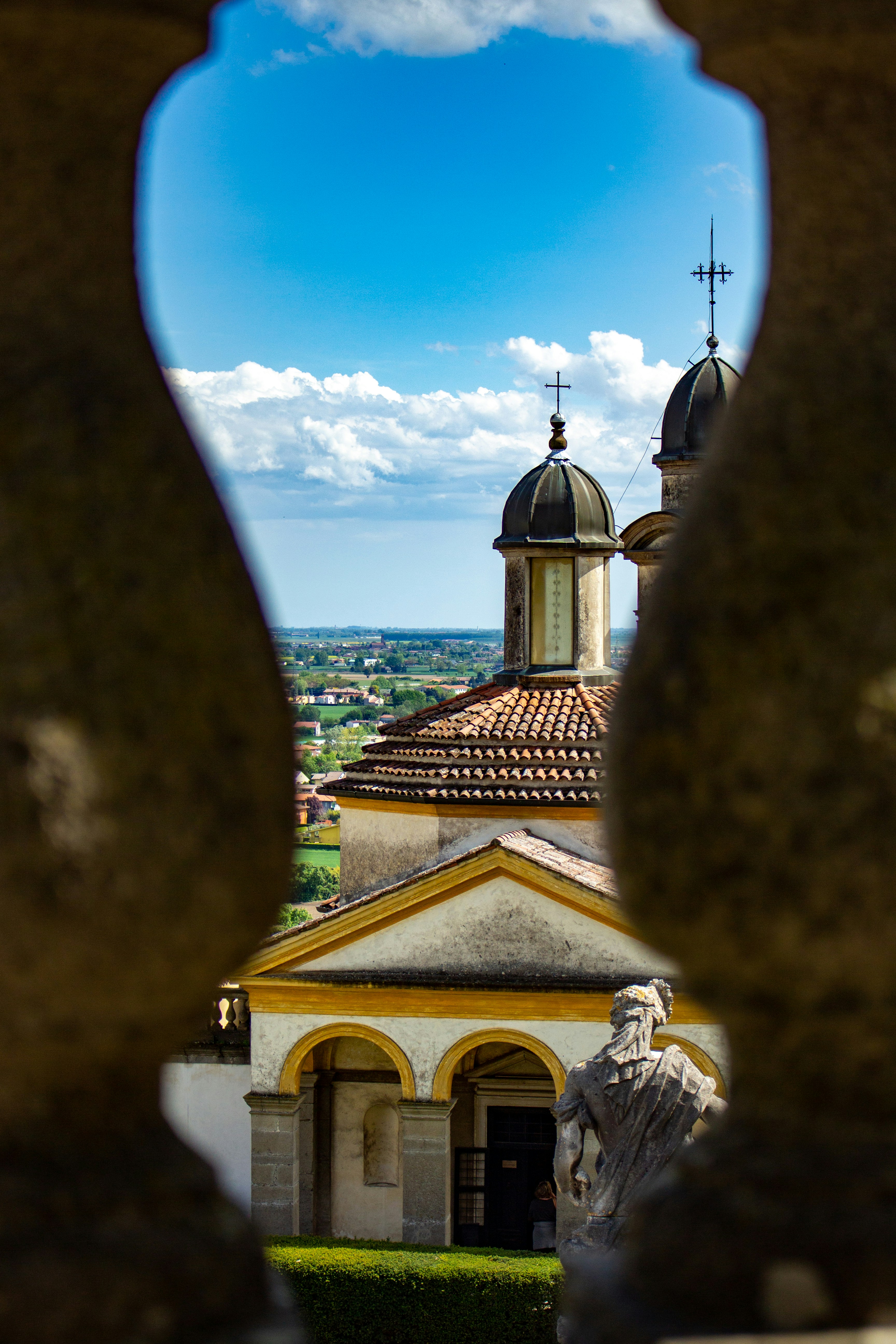 View of a historic building with domed rooftops framed by an archway, showcasing a vibrant landscape beyond.