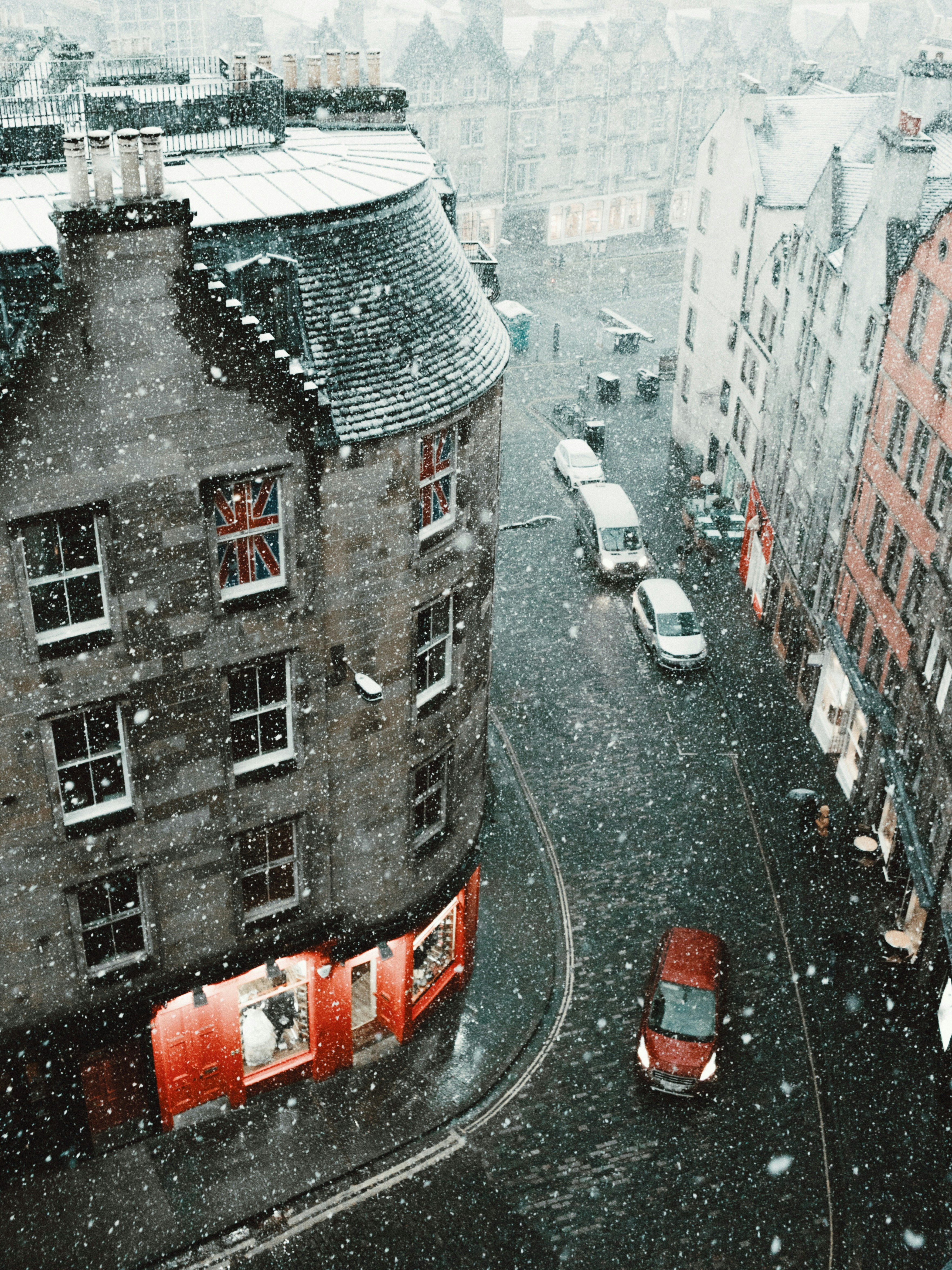 Snowfall over a Curved Corner: Red Facade on a Narrow European Street
