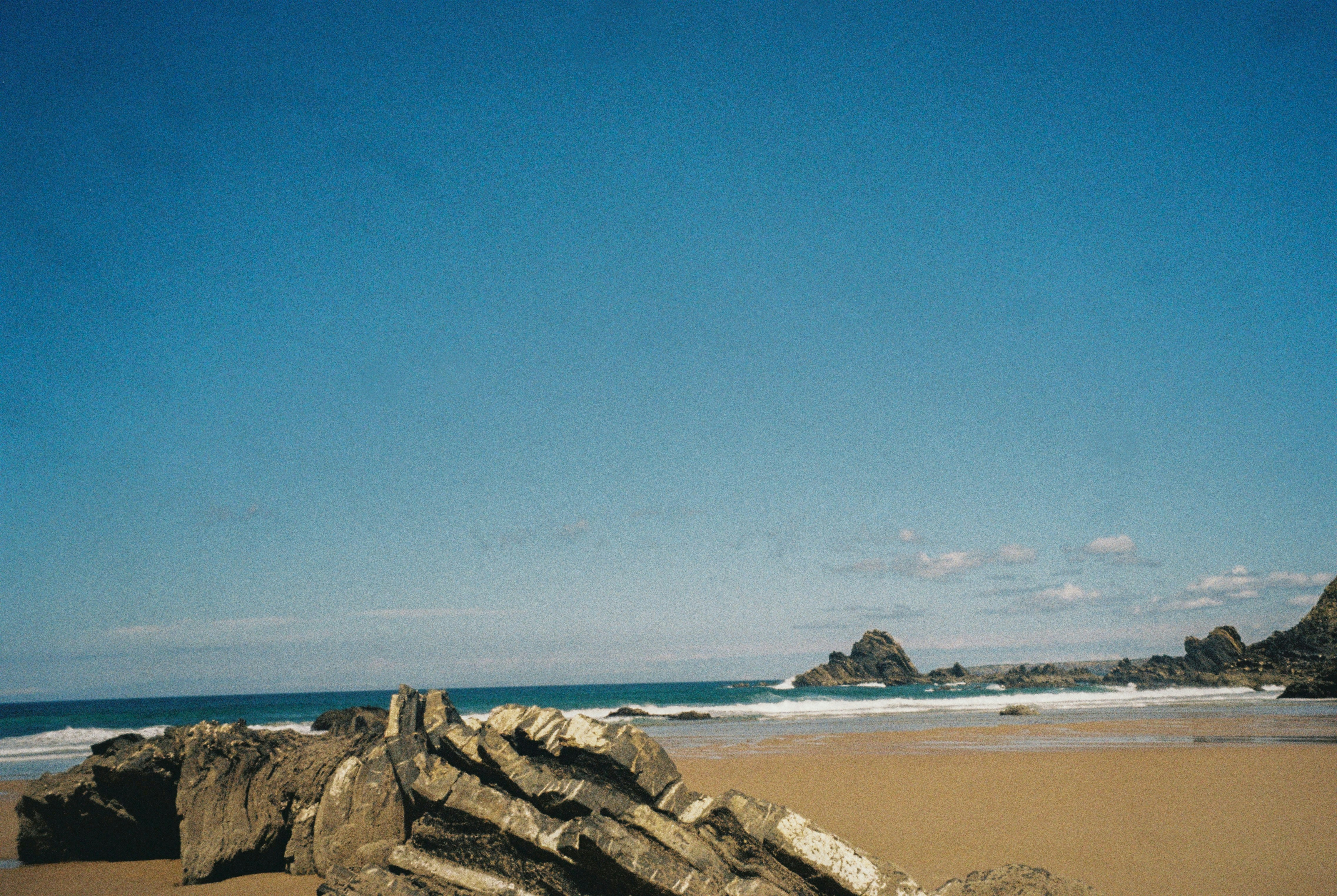 A surfboard is laying on a rock on the beach photo – Free Zambujeira do ...