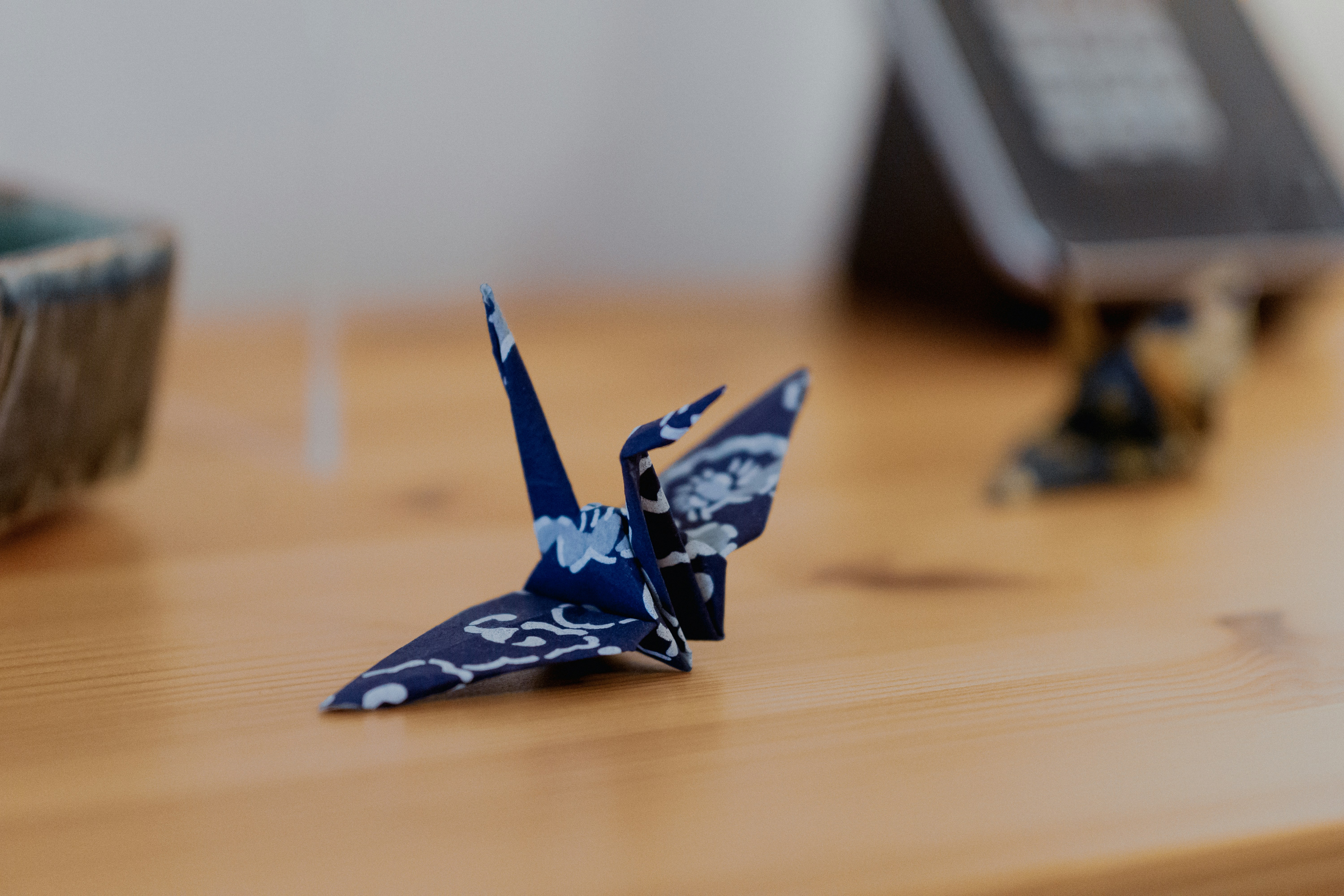 Intricately folded origami crane made from patterned paper, resting on a wooden surface surrounded by subtle decor elements.