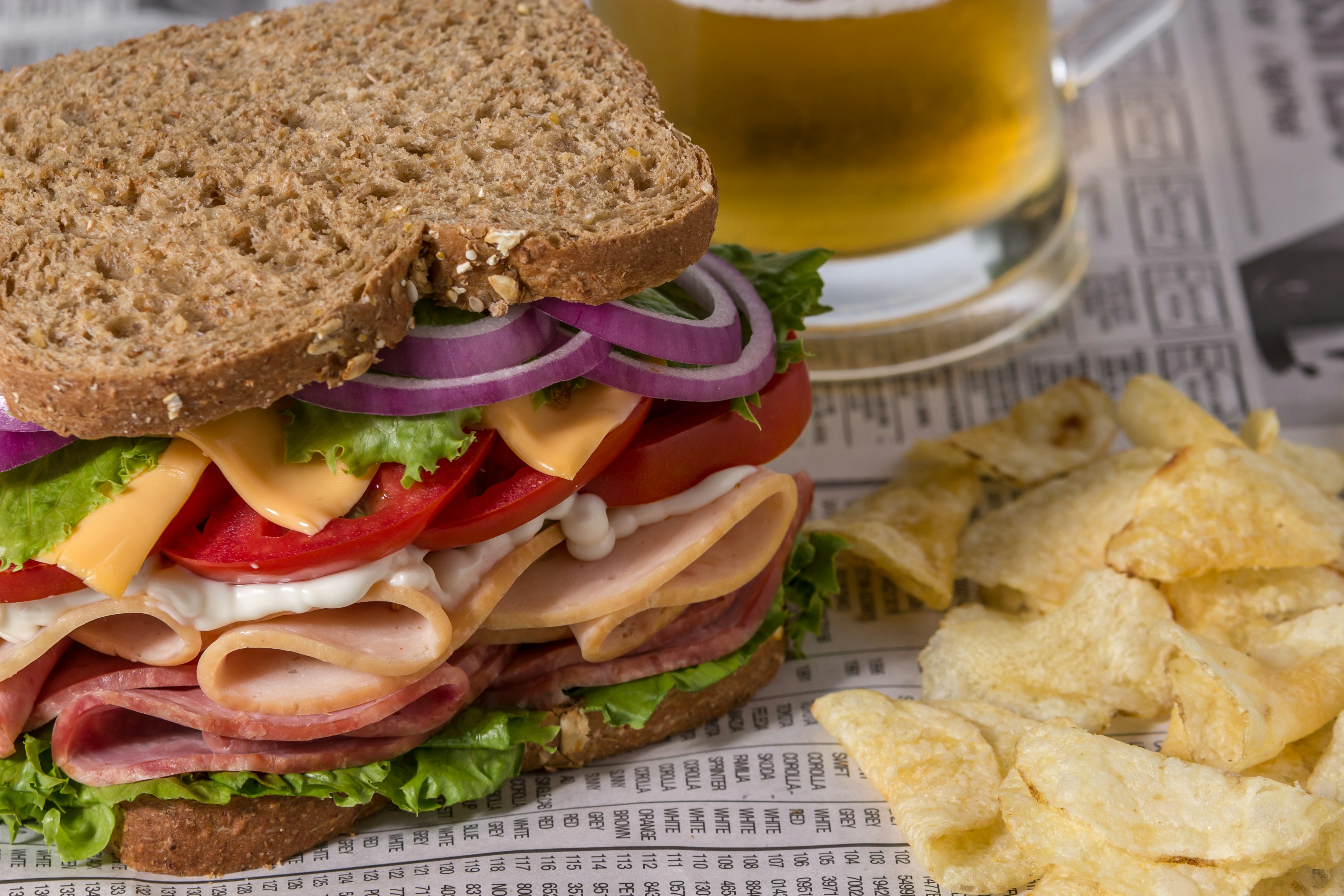 A sandwich and chips on a newspaper with a glass of beer photo – Free ...