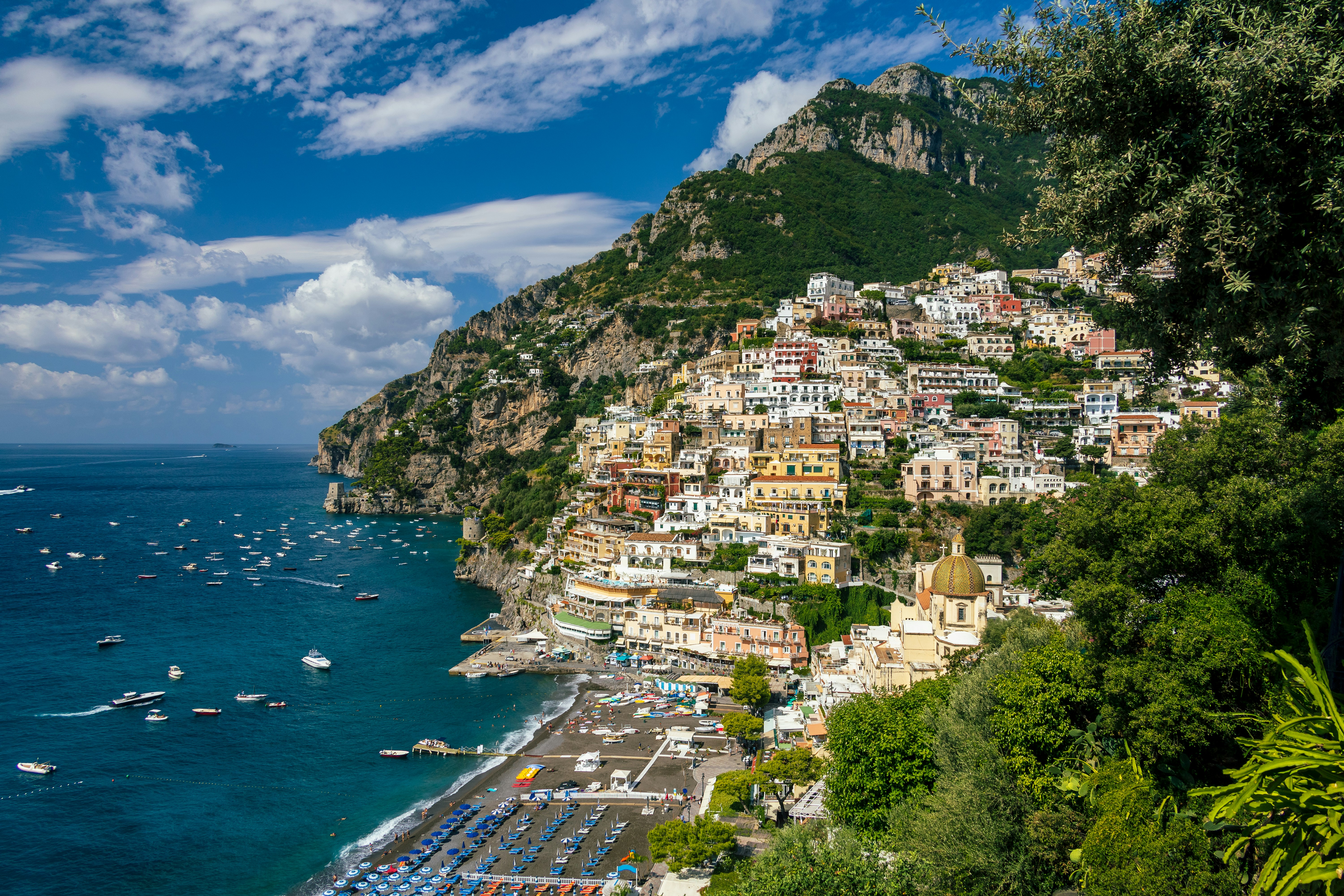 Colorful hillside village along the Amalfi Coast with boats scattered across the blue sea.