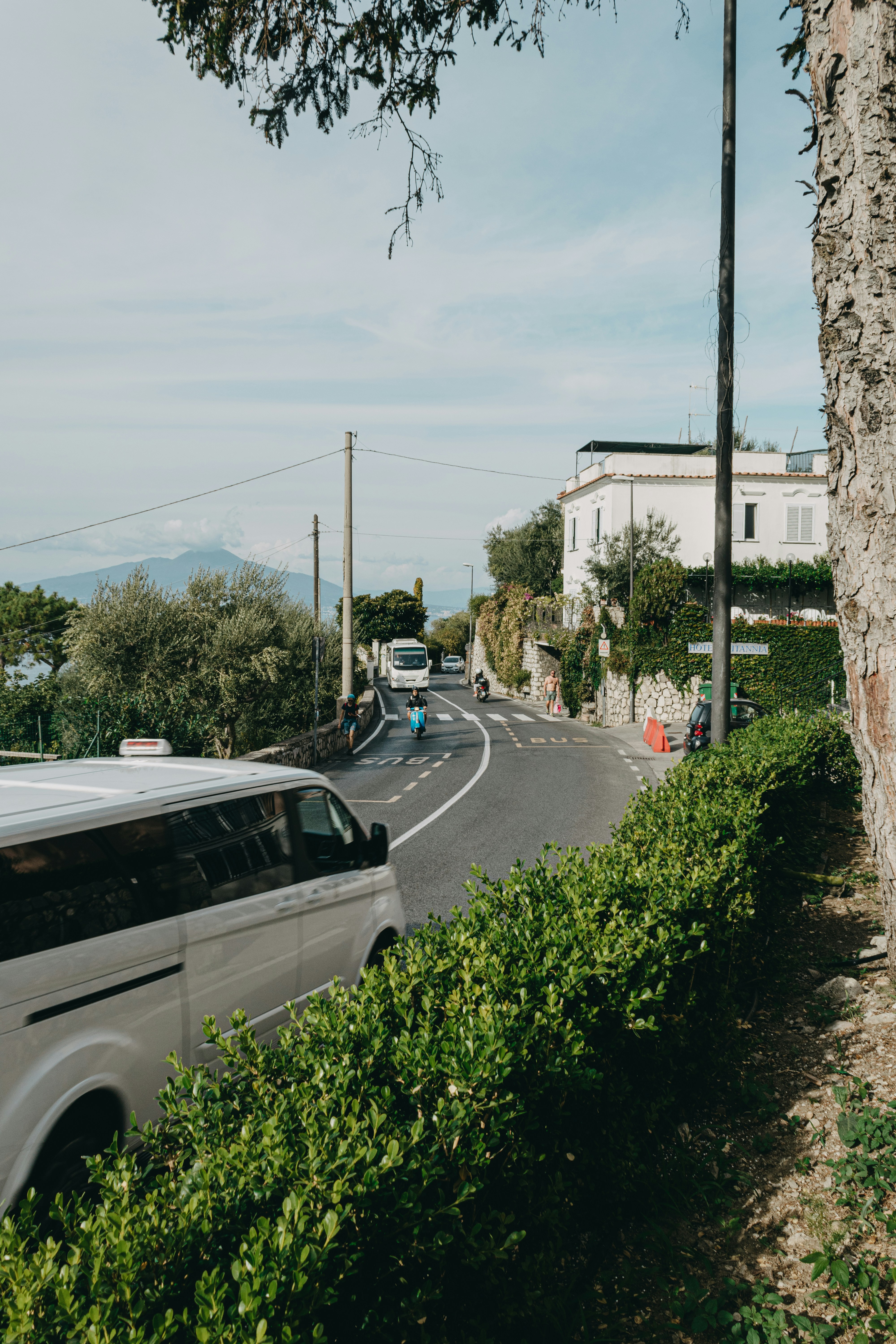 Sunlit Hillside Street: White Facade, Green Hedge, and a Moving Van