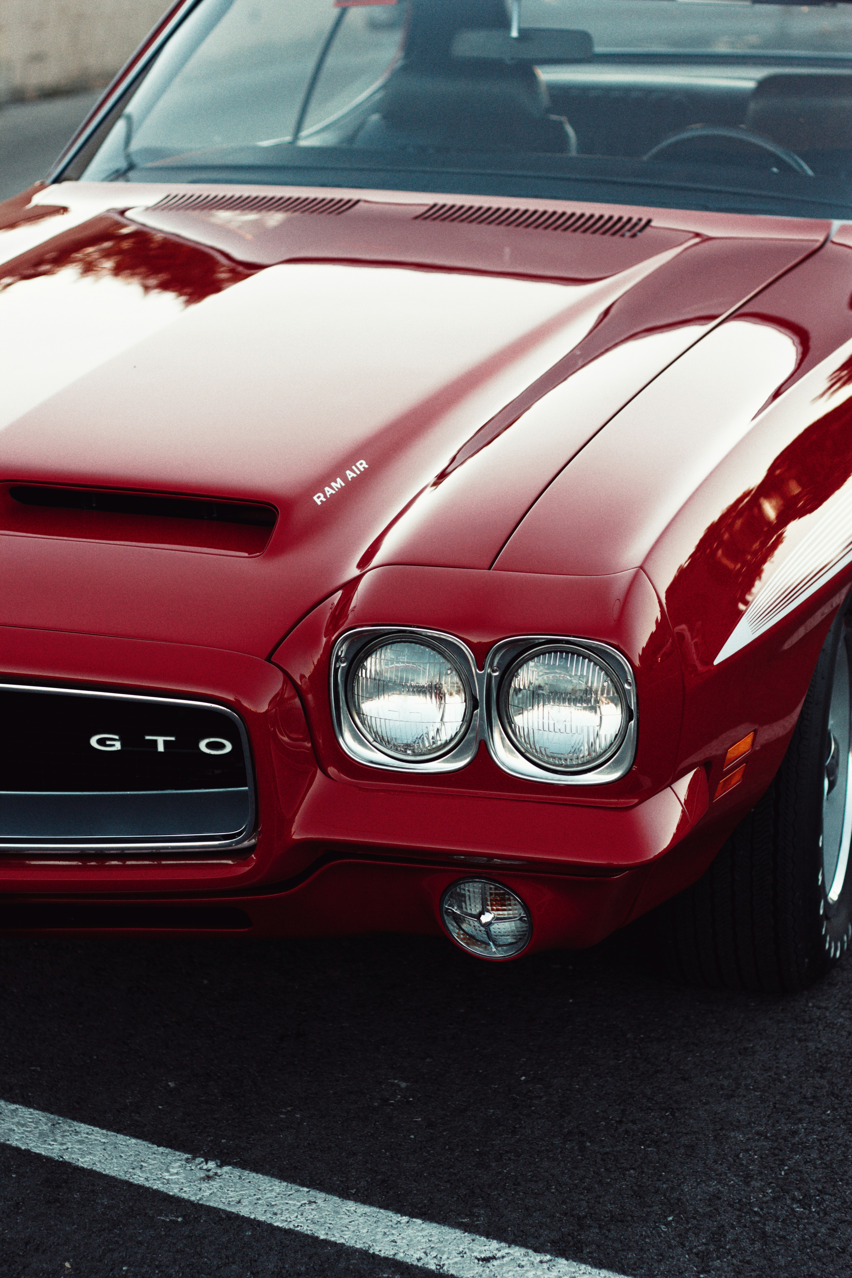 Close-up of a vintage red GTO showcasing its iconic grille and headlights. The car's sleek lines and polished surface reflect its classic design.