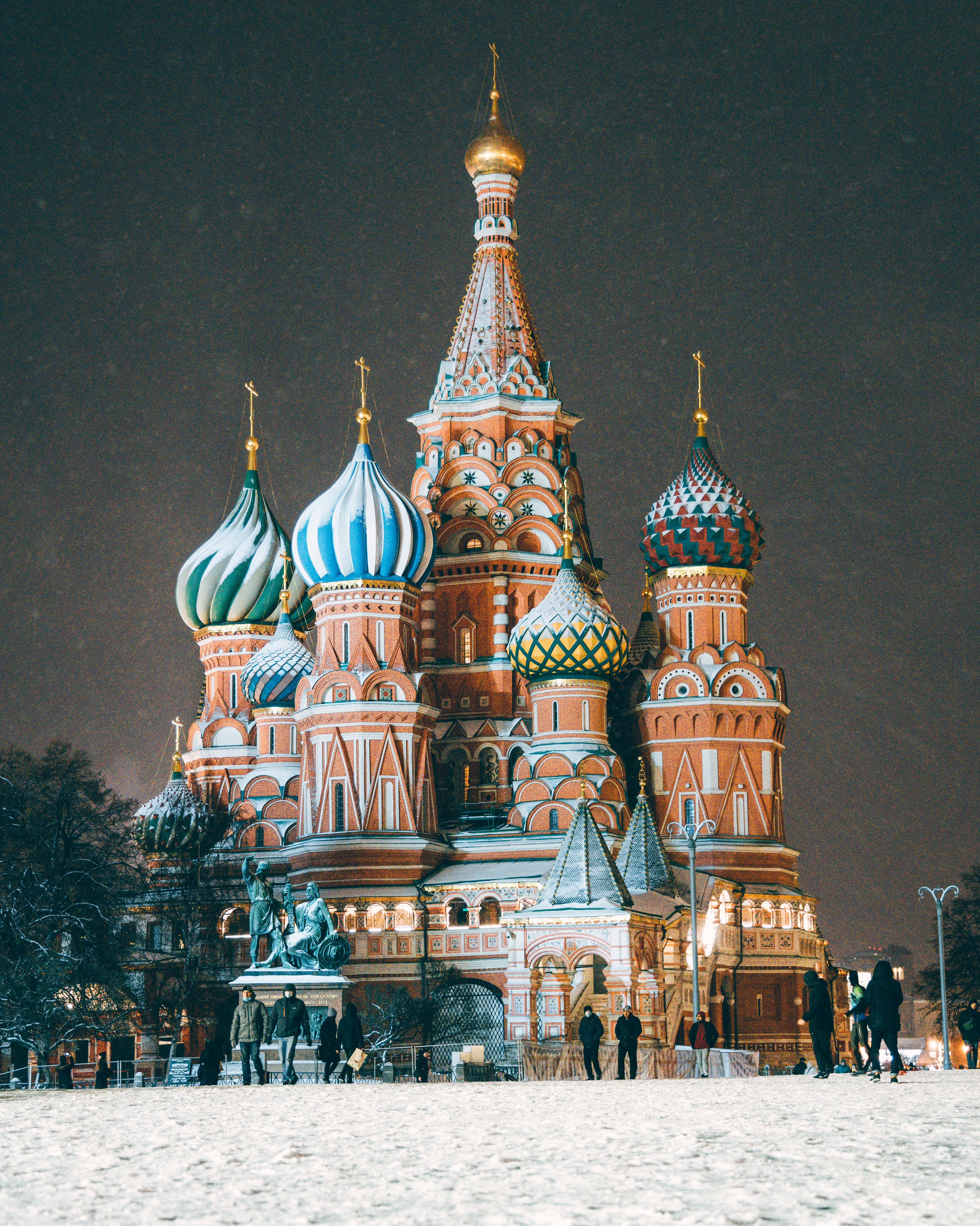 Colorful onion domes of St. Basil's Cathedral rise majestically against a snowy backdrop, with visitors strolling nearby.