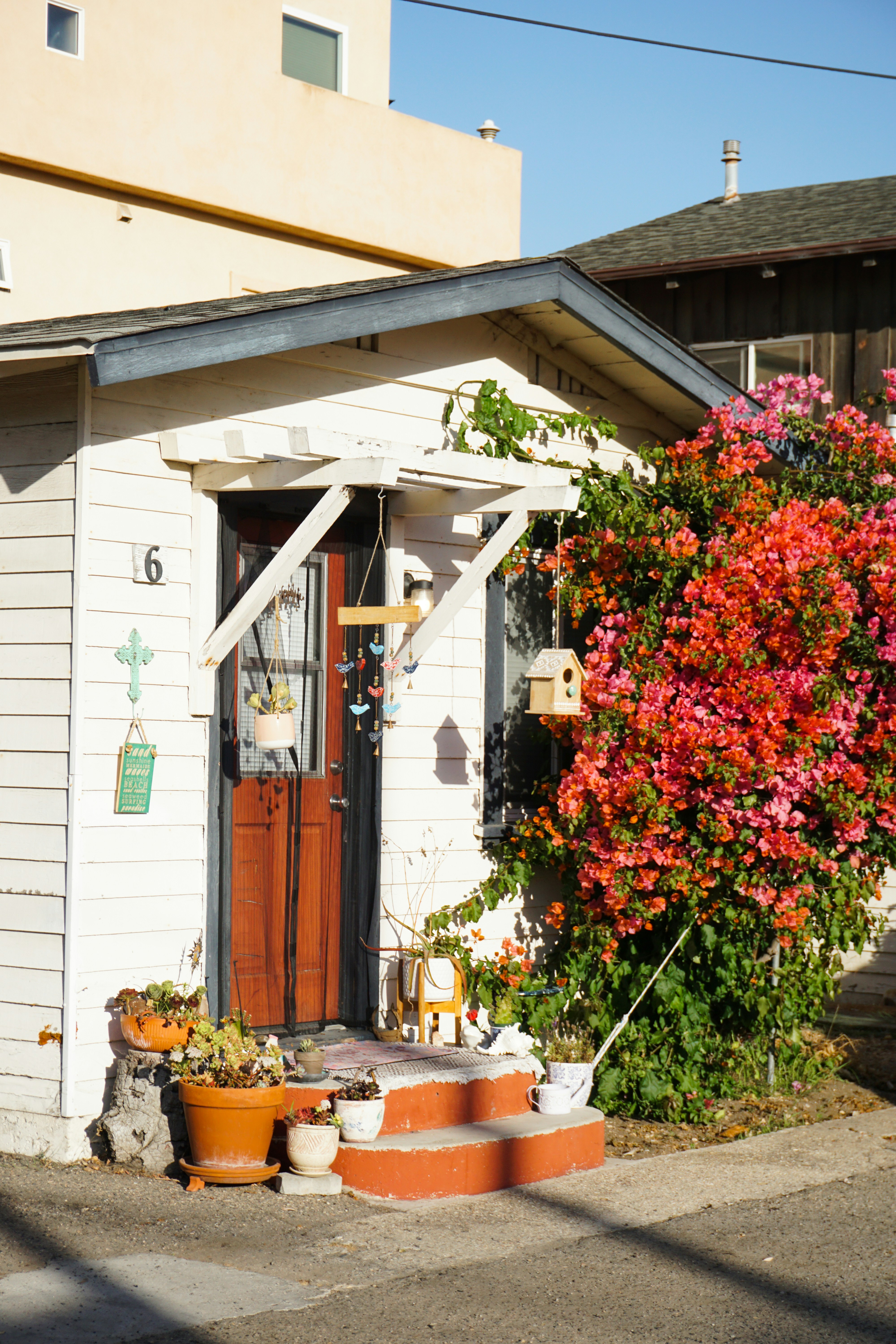 A quaint house adorned with vibrant bougainvillea, showcasing a welcoming entrance with potted plants and decorative elements.