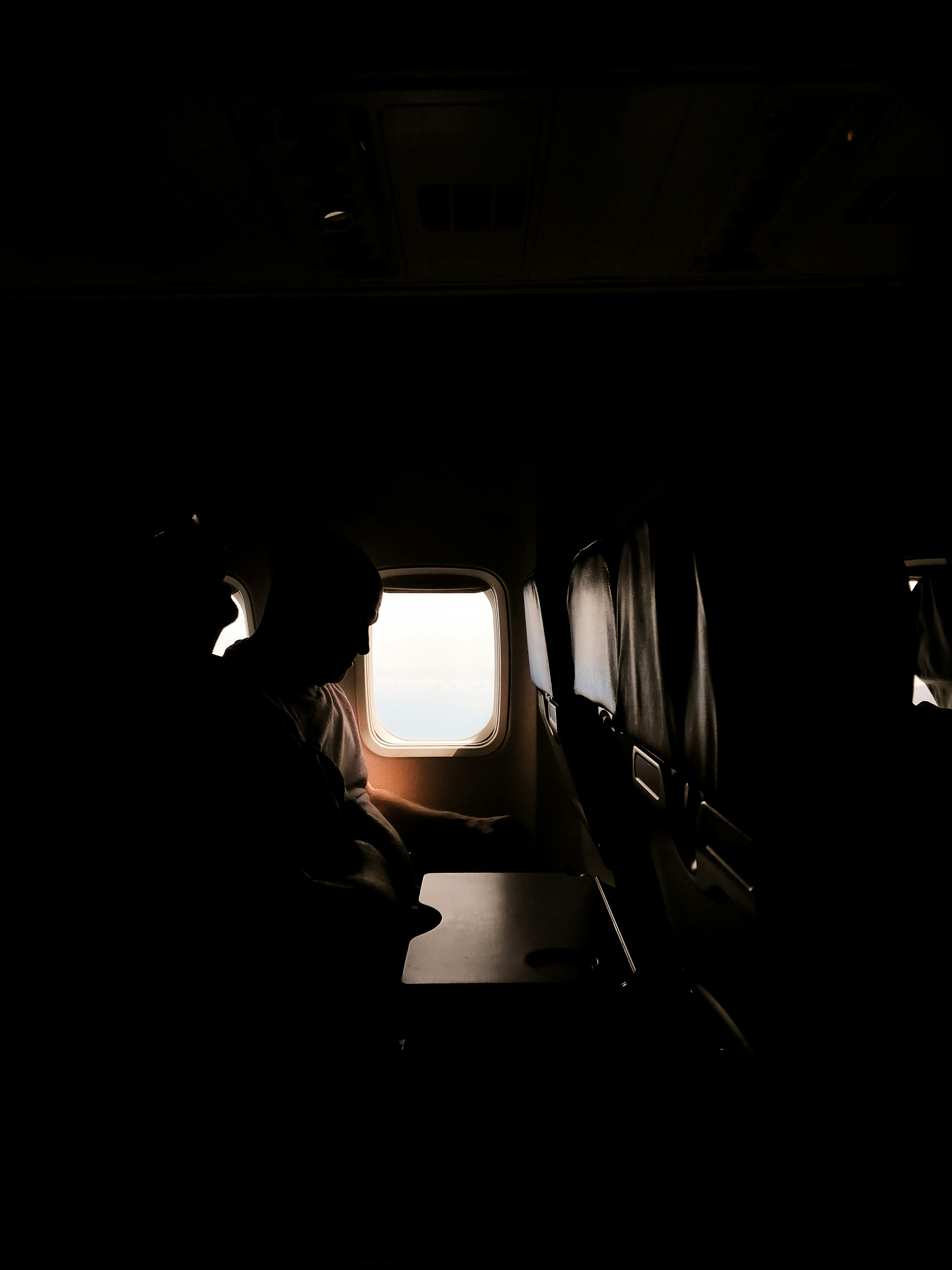 Silhouetted passenger seated by an airplane window, gazing out at the horizon, with soft light illuminating the cabin.