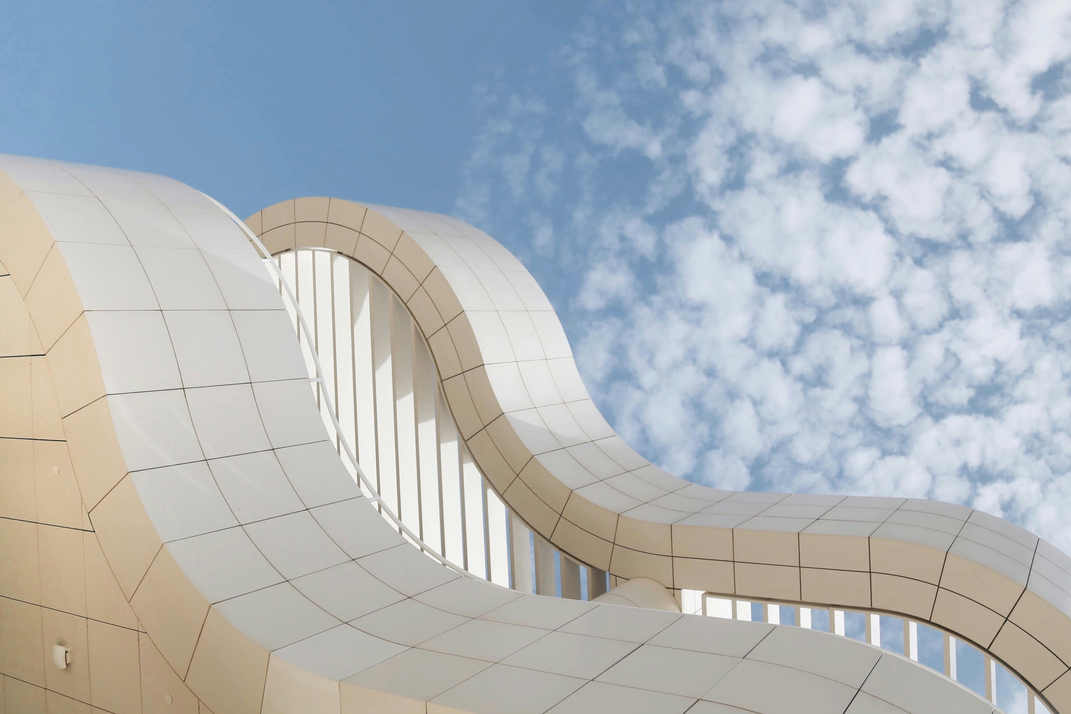 Architectural structure with flowing curves against a backdrop of blue sky and wispy clouds.