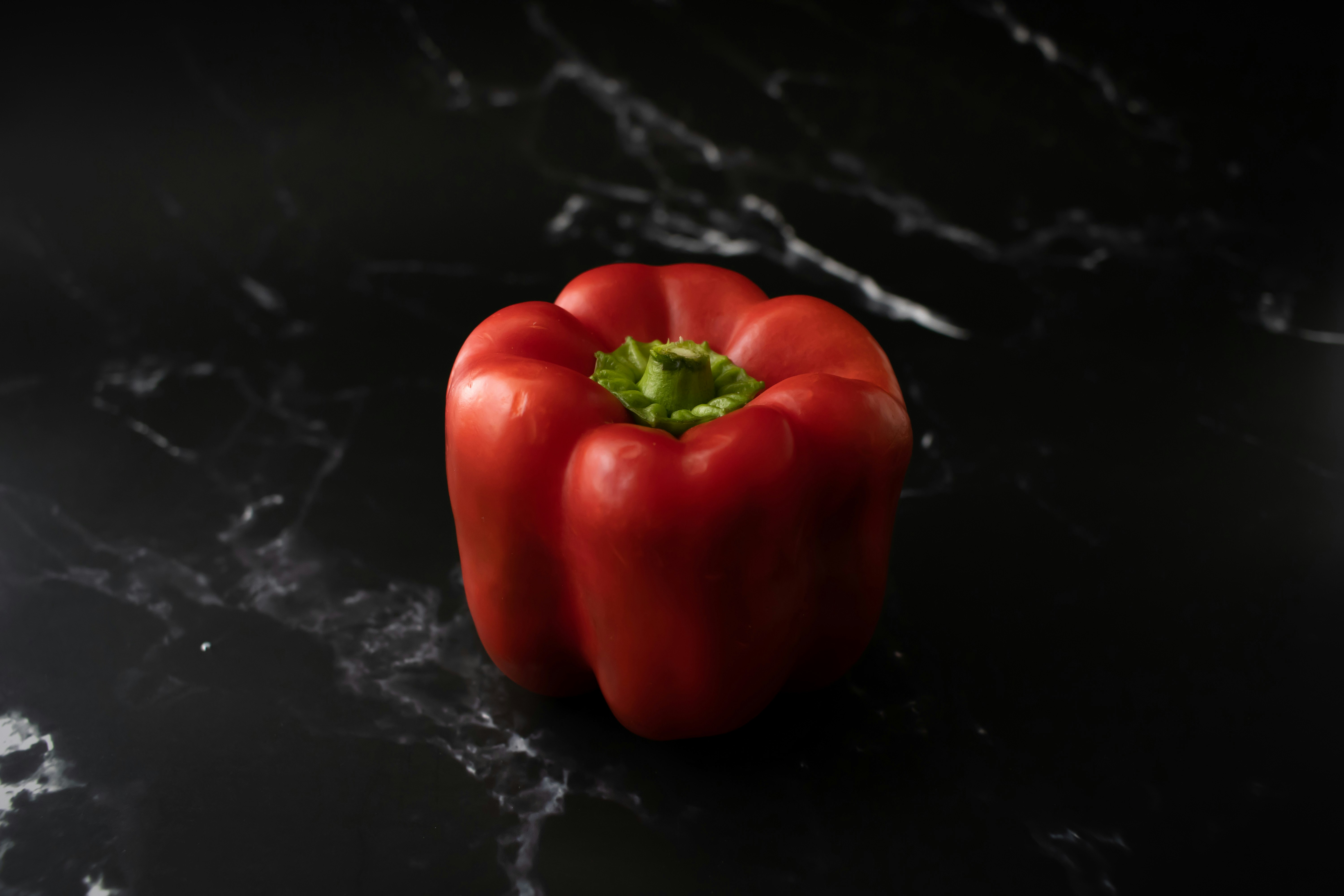 Vibrant red bell pepper resting on a sleek black marble surface, highlighting its glossy texture and fresh appearance.