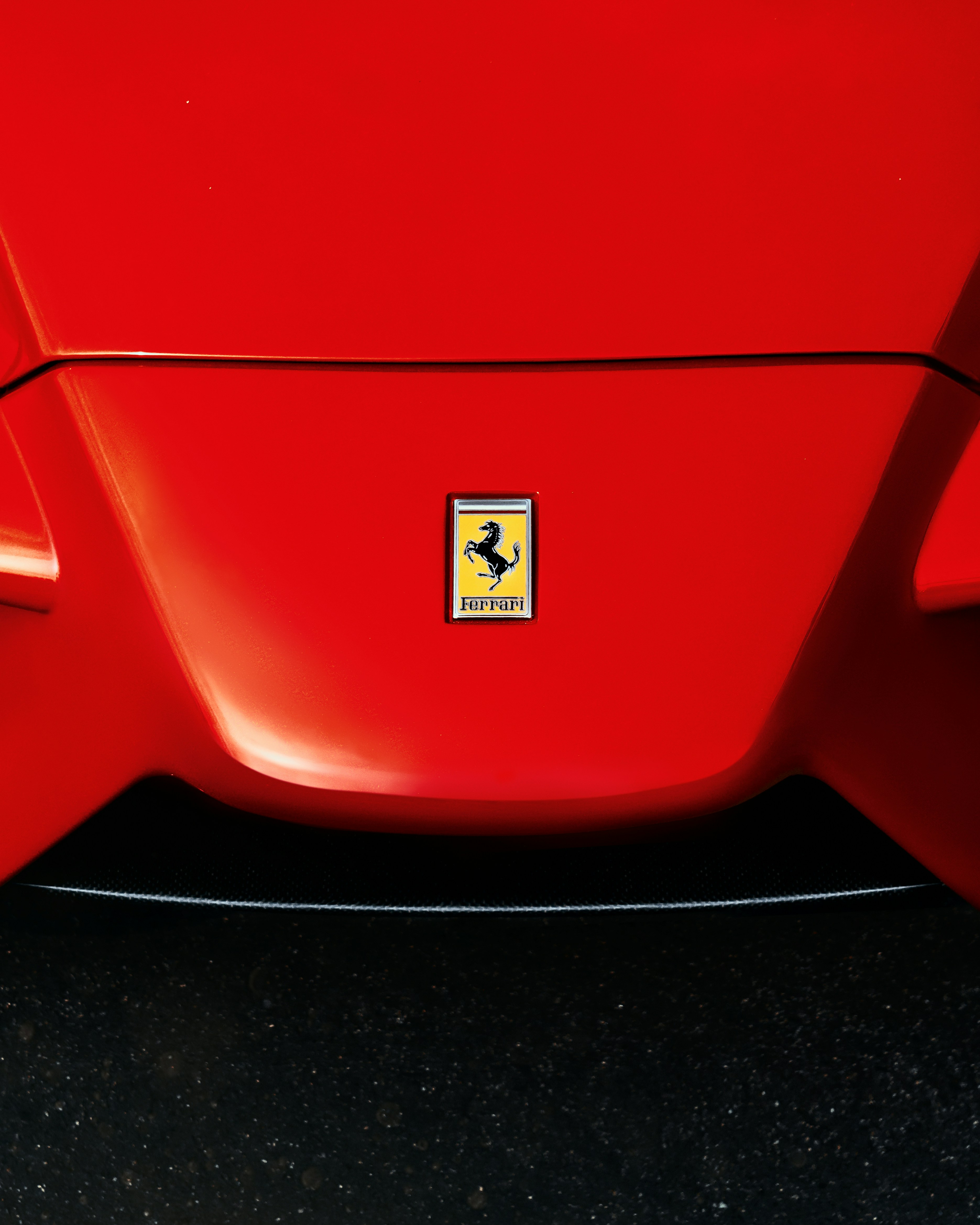 Close-up of a Ferrari emblem on a vibrant red car hood, showcasing the sleek design and craftsmanship.