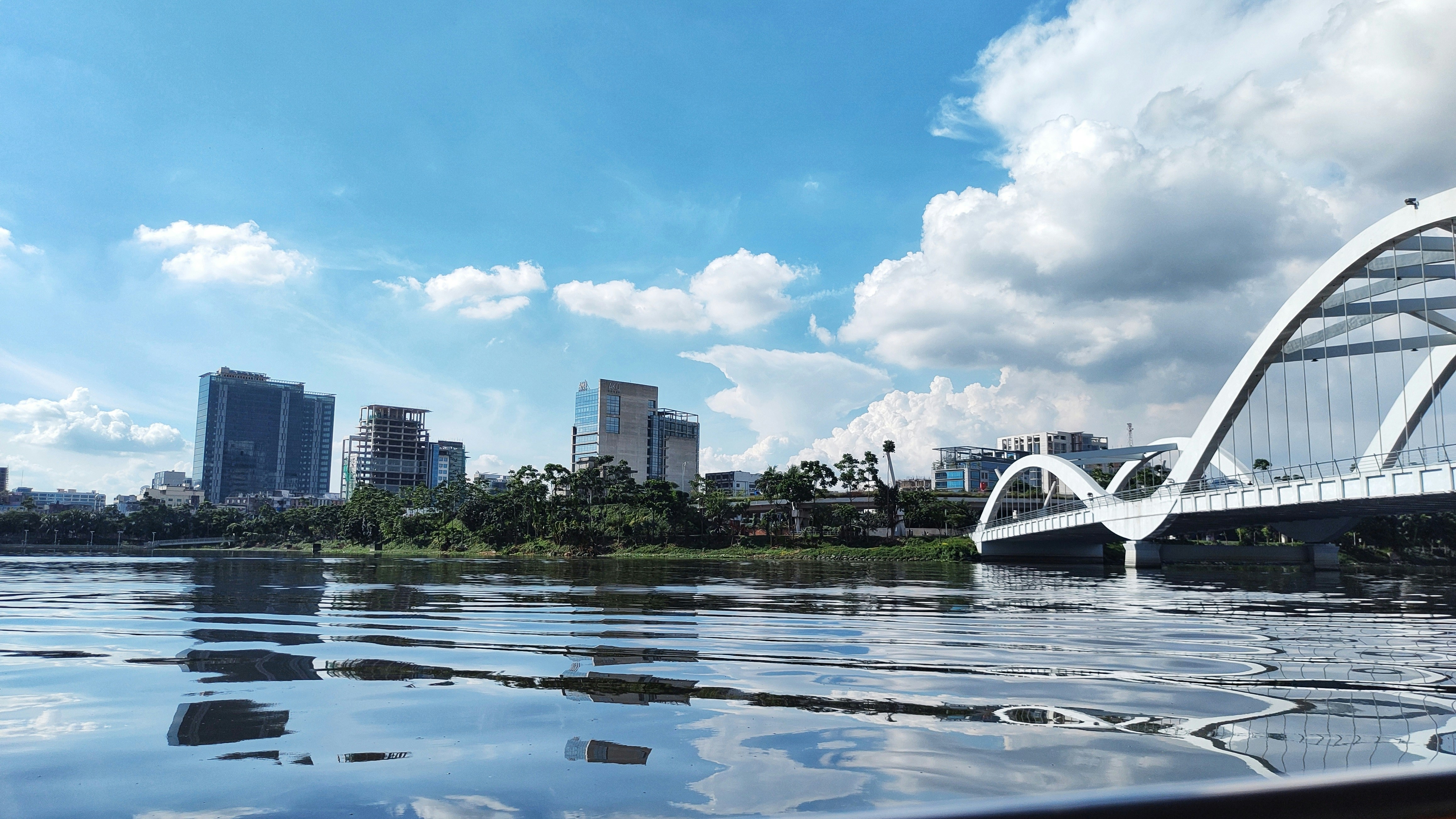 Modern city skyline reflecting on calm waters under a vibrant sky with scattered clouds.