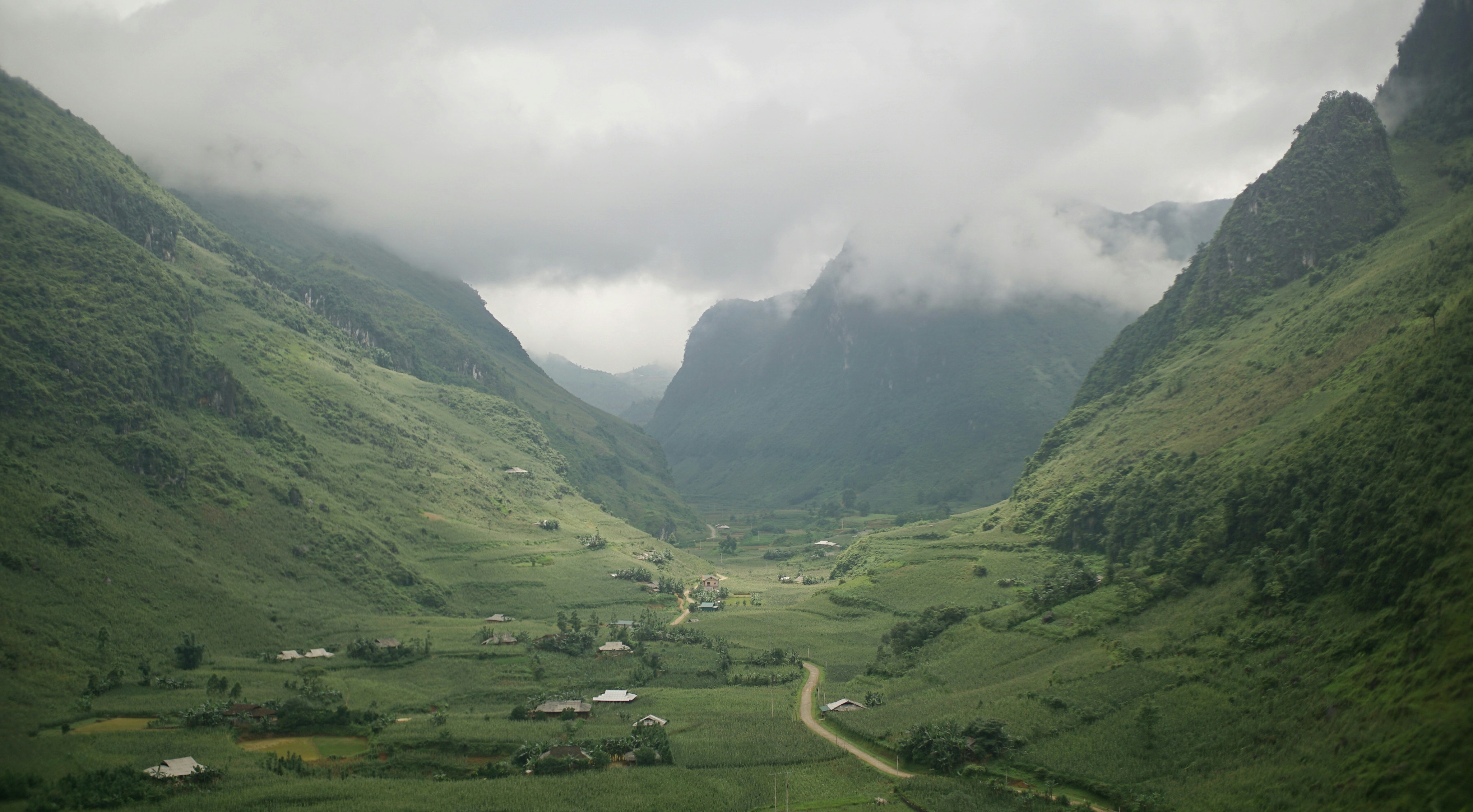 Lush green valley with small settlements nestled between towering, mist-shrouded mountains.