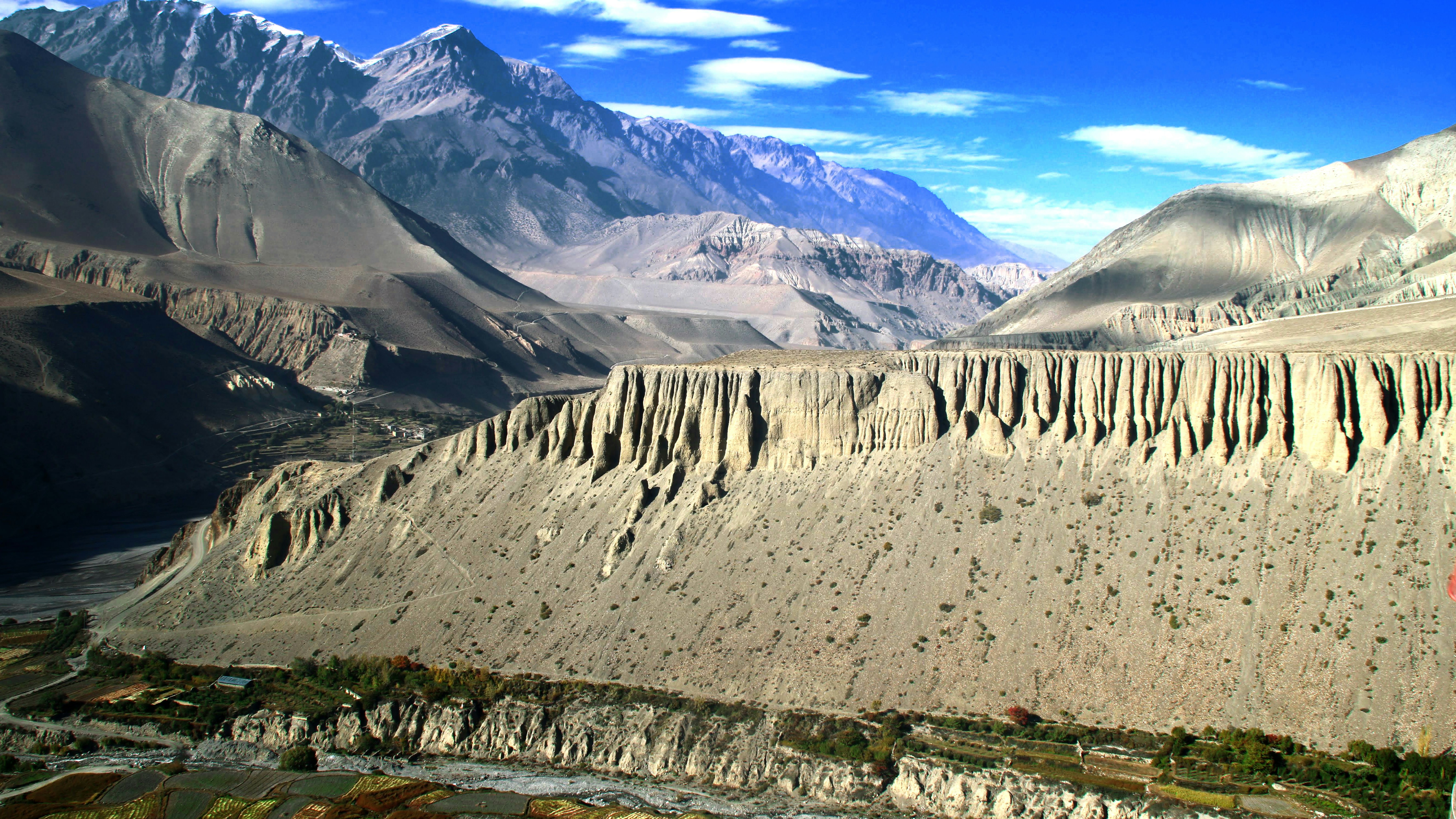 Aerial view of rugged mountain terrain showcasing dramatic cliffs and valleys under a clear blue sky.