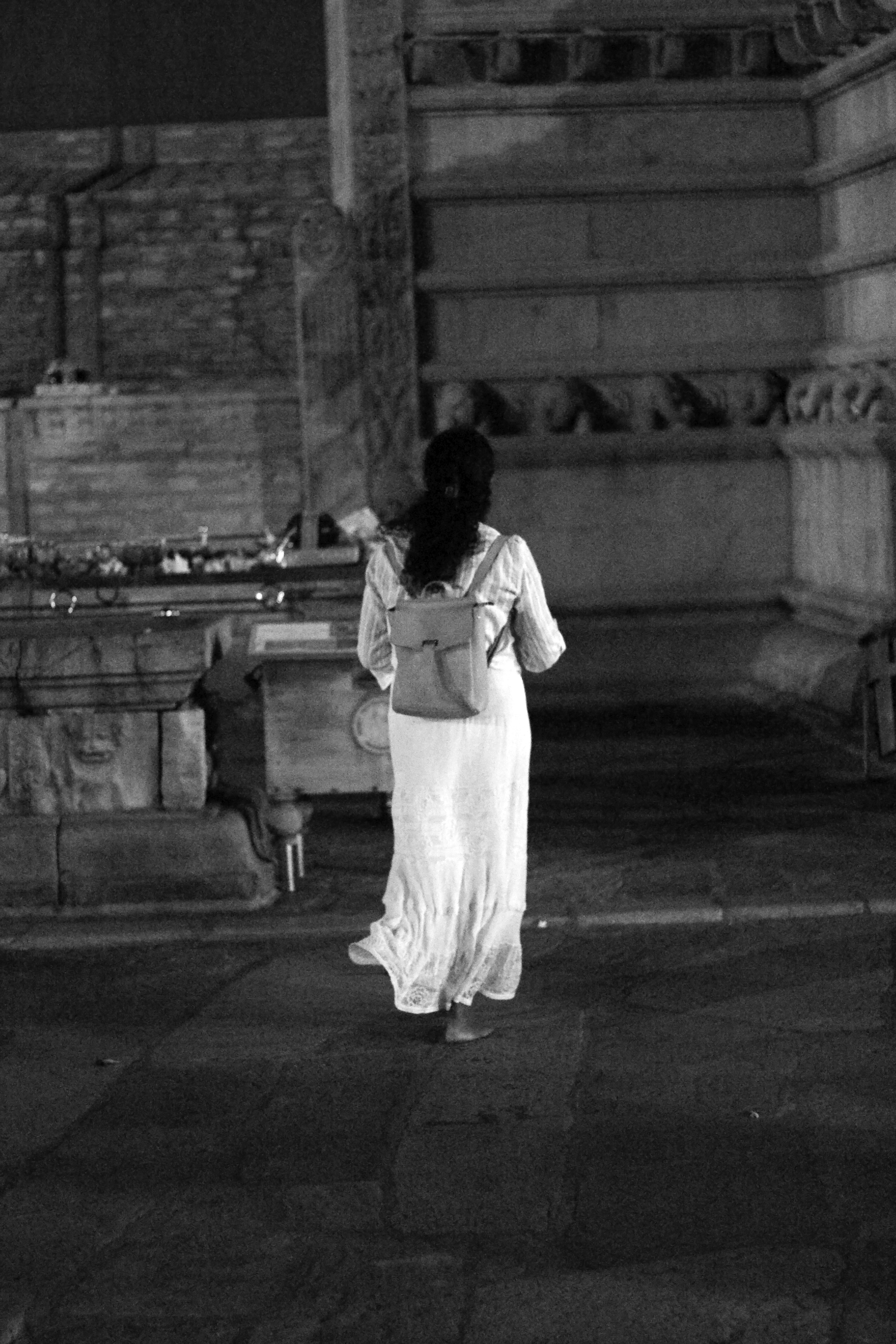 Woman in flowing white dress walks toward ancient stone stairs at night